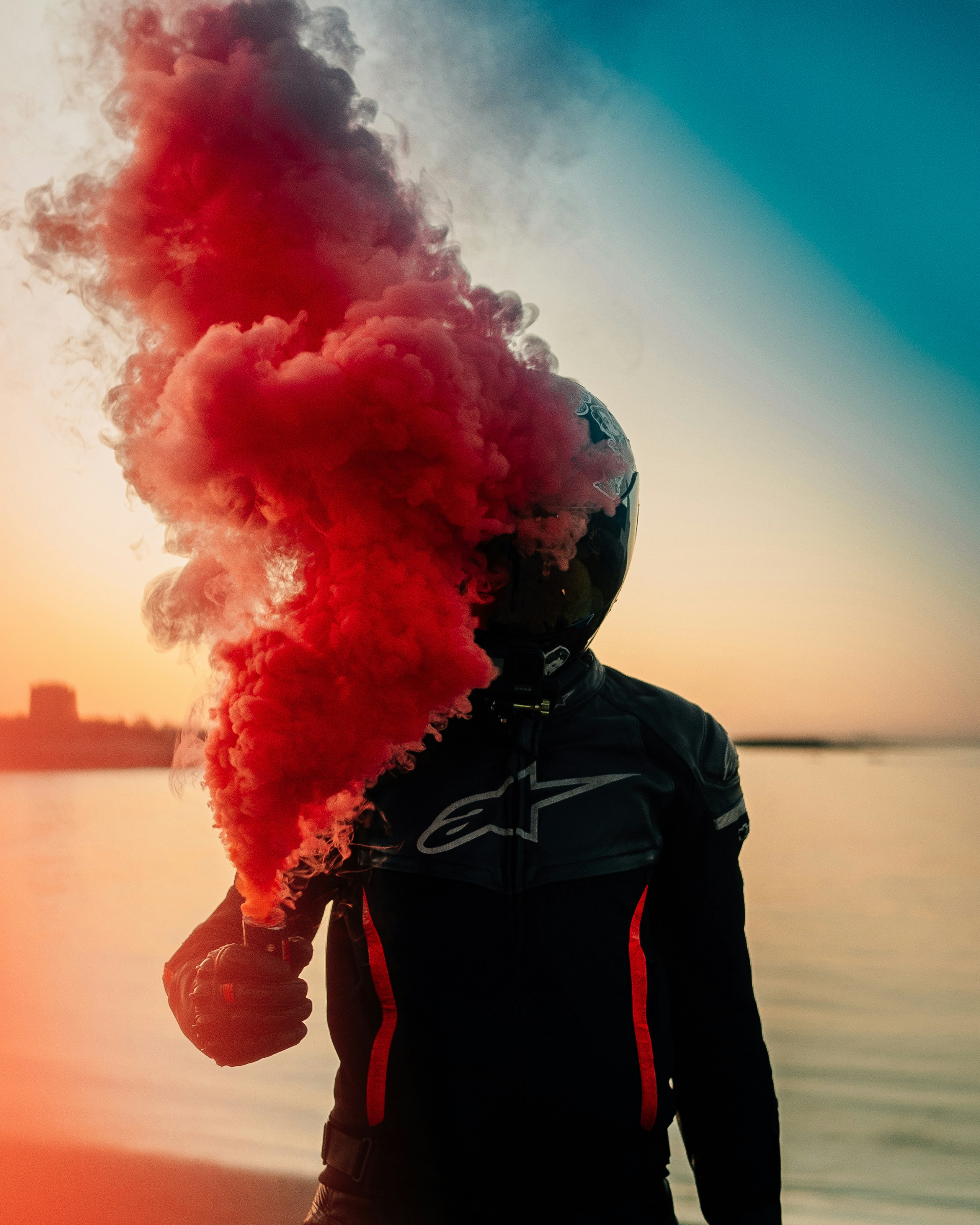 Motorcyclist holding a red smoke grenade against a sunset backdrop, creating a dramatic and vibrant atmosphere.