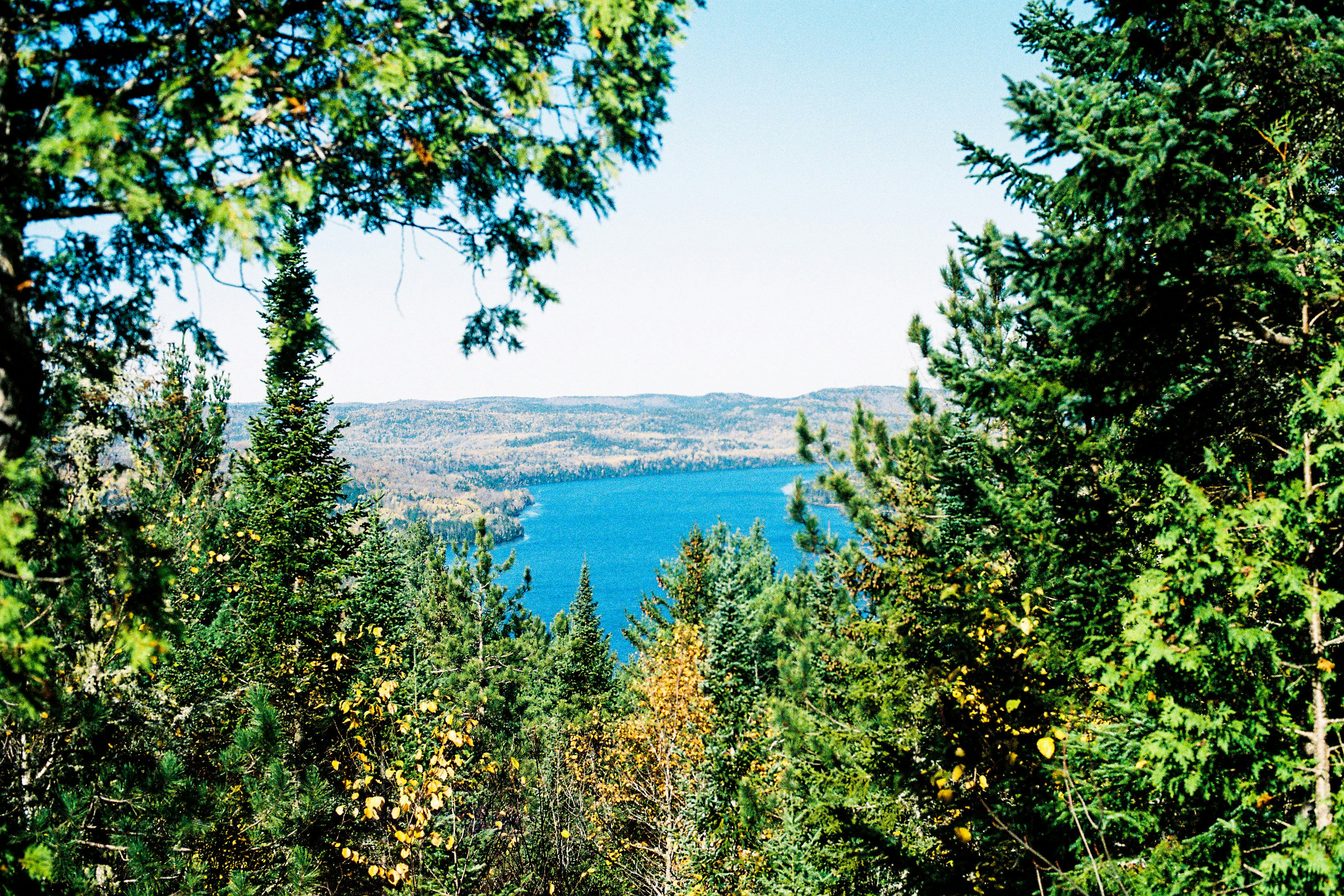 Vibrant autumn foliage frames a tranquil lake nestled among rolling hills under a clear blue sky.