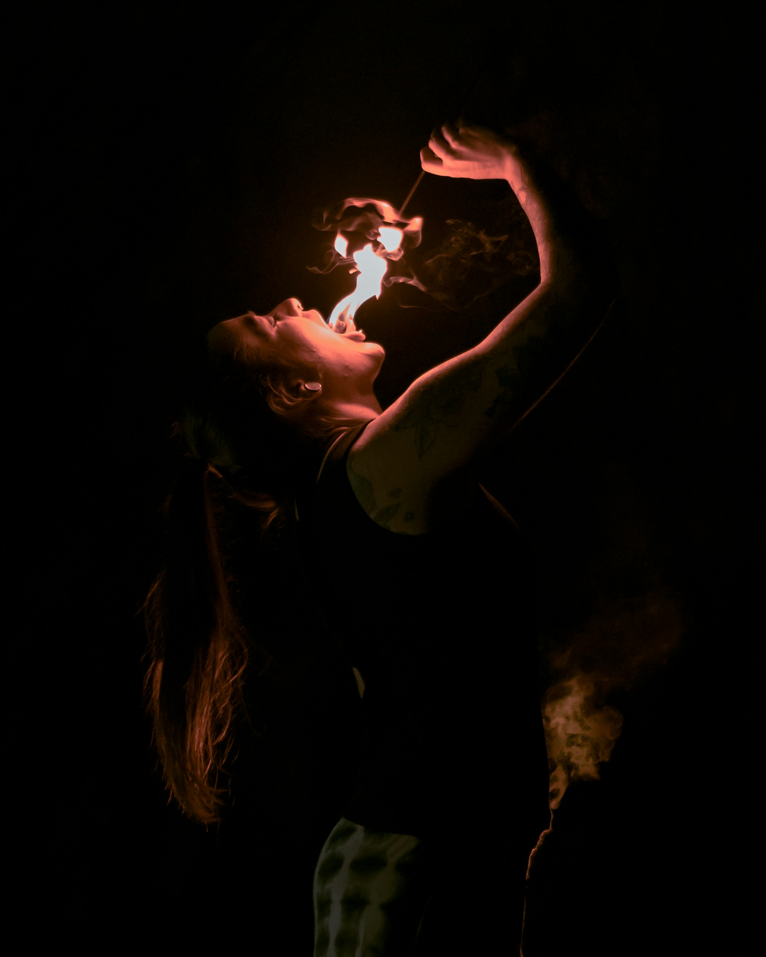 A performer ignites flames from their mouth, silhouetted against a dark backdrop, showcasing the art of fire breathing.