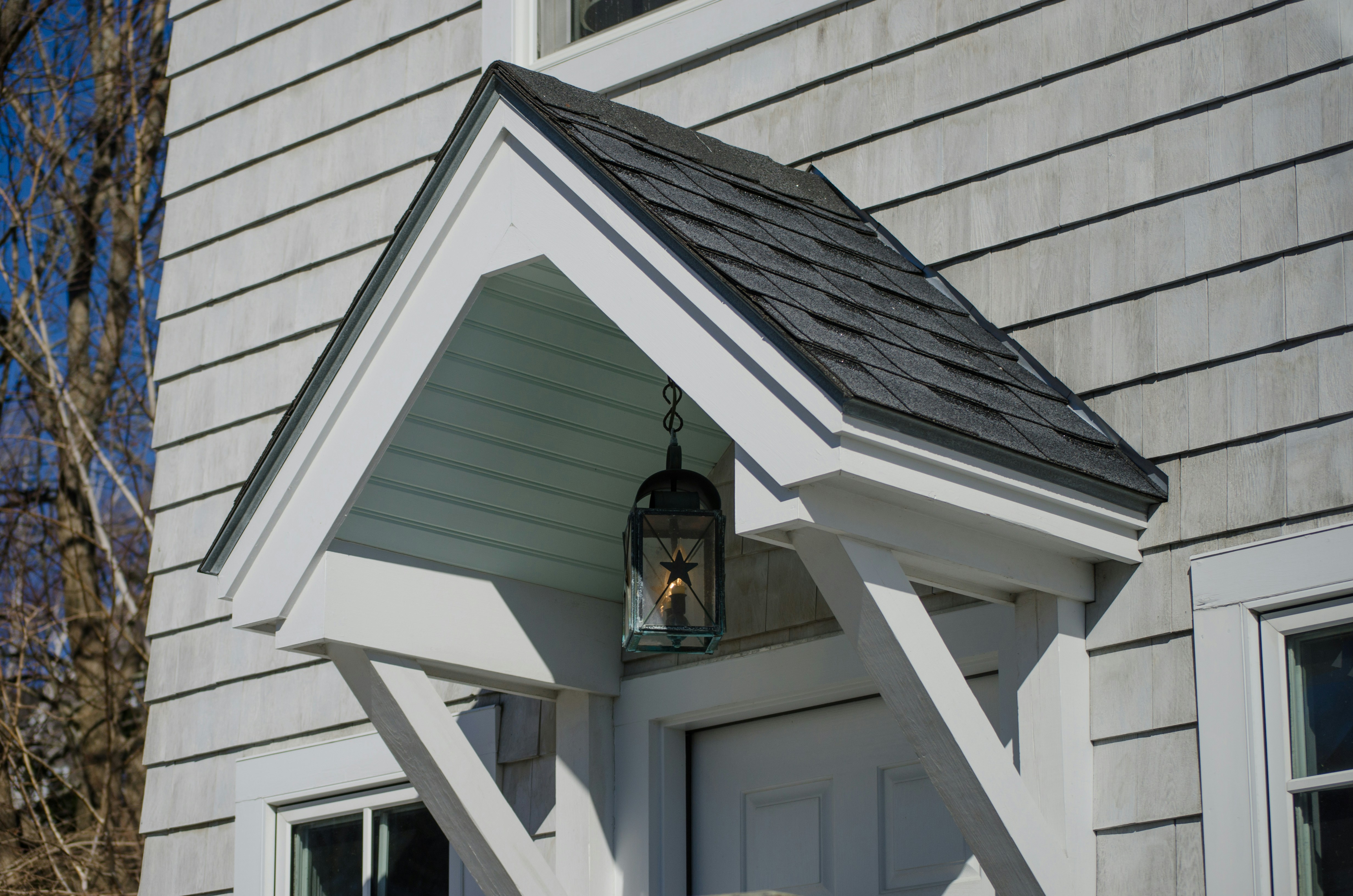 Lantern under a white gable frames the inviting entry on a sunlit clapboard house