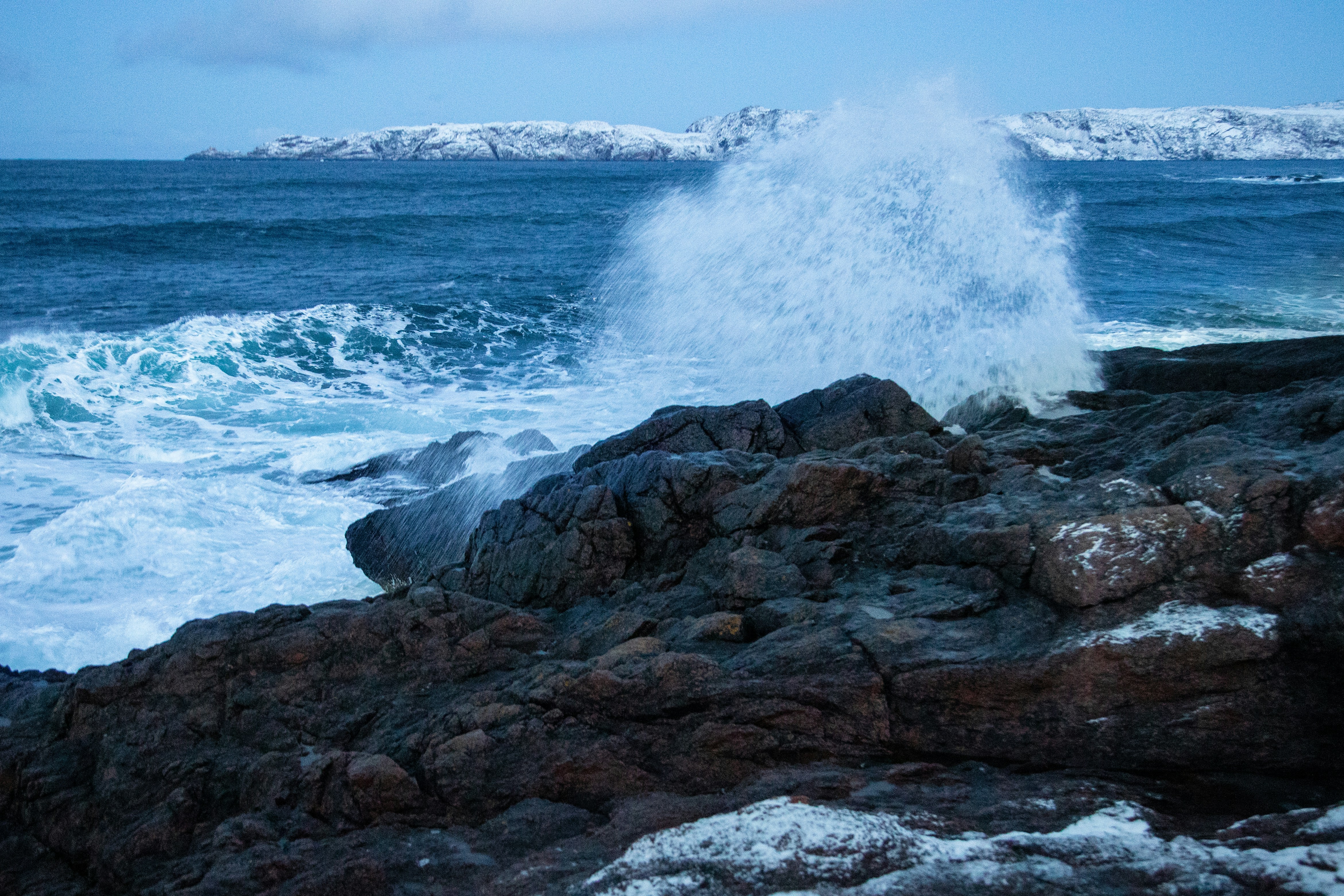 Powerful waves crashing against rocky coastline under a twilight sky.