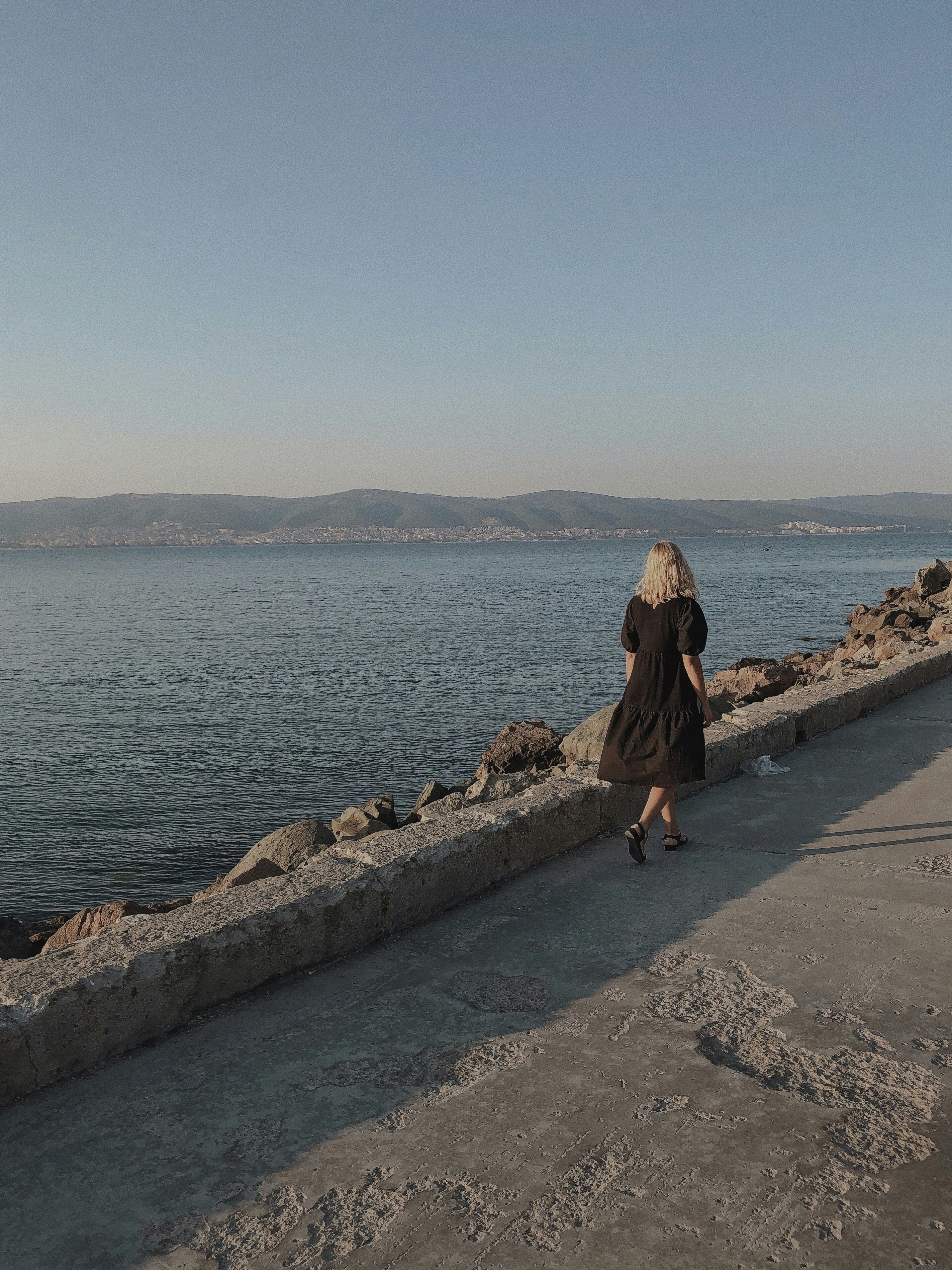 A Quiet Promenade: Woman in Black Walks the Pier at Dusk