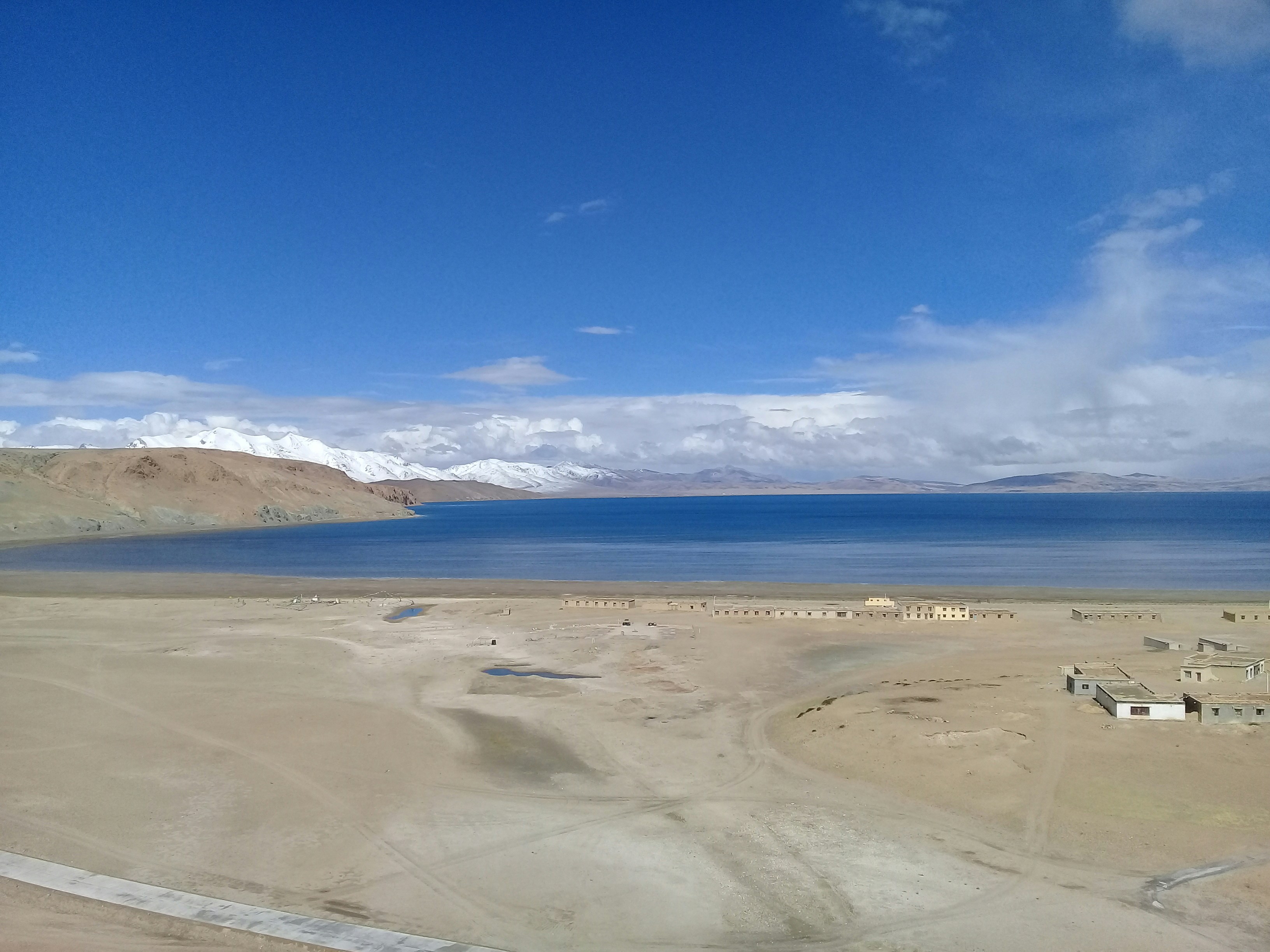 Vast landscape featuring a tranquil lake bordered by mountains under a clear blue sky. The scene captures the harmony of nature and solitude.