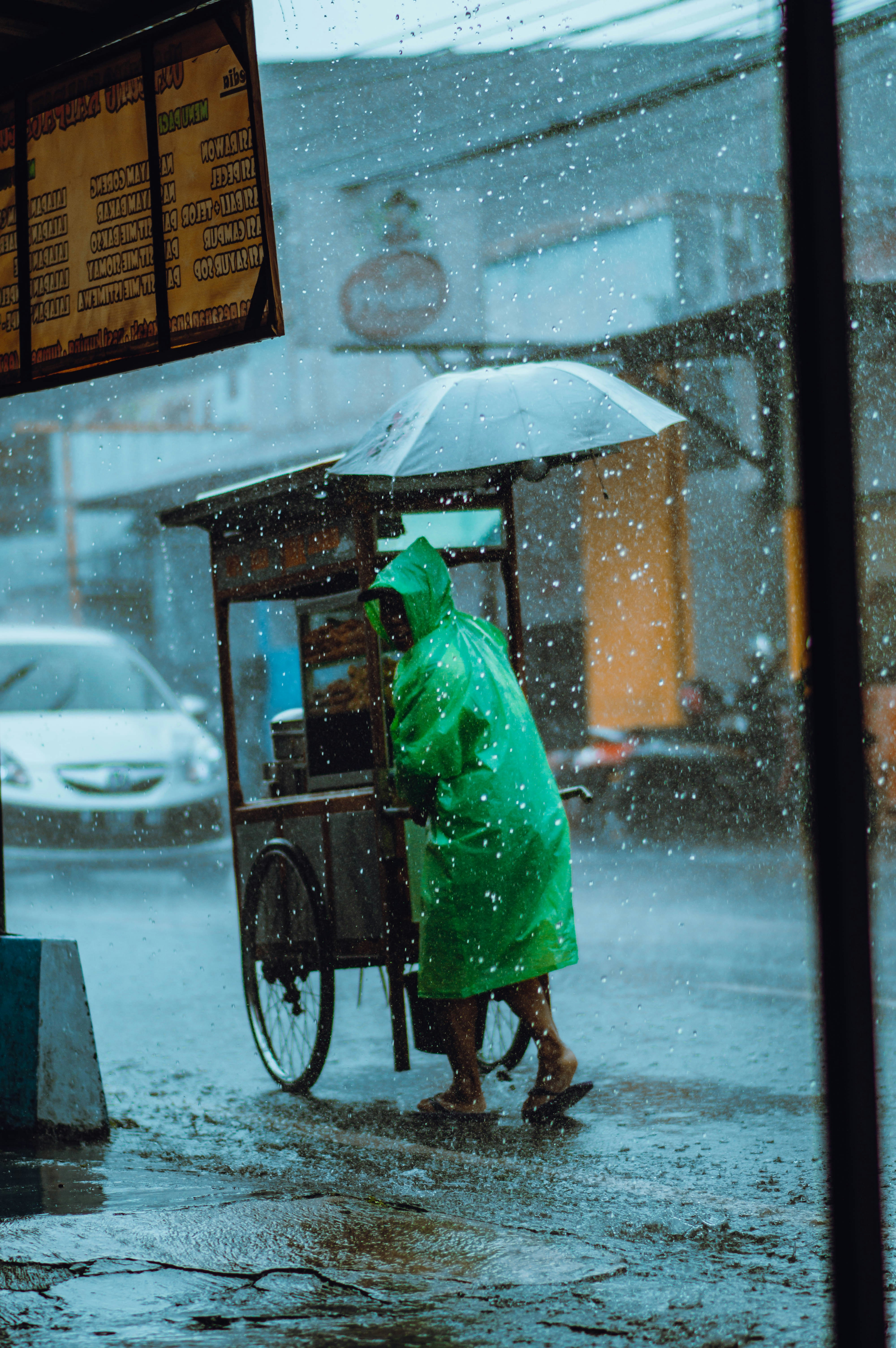 Green Rain, Blue Street: A Hooded Vendor in the Downpour