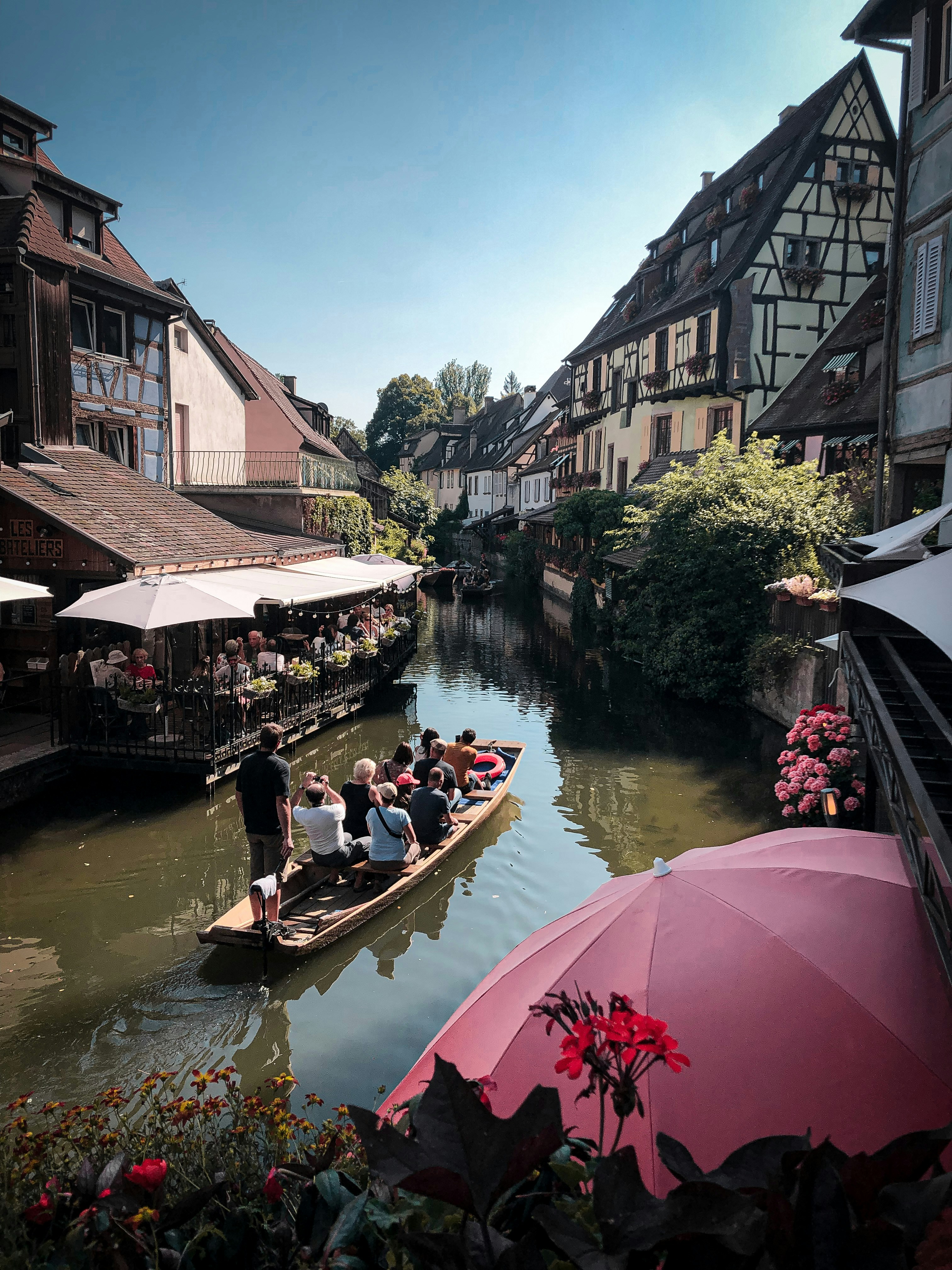 Tourists enjoying a leisurely boat ride along a picturesque canal lined with charming houses and vibrant flora.
