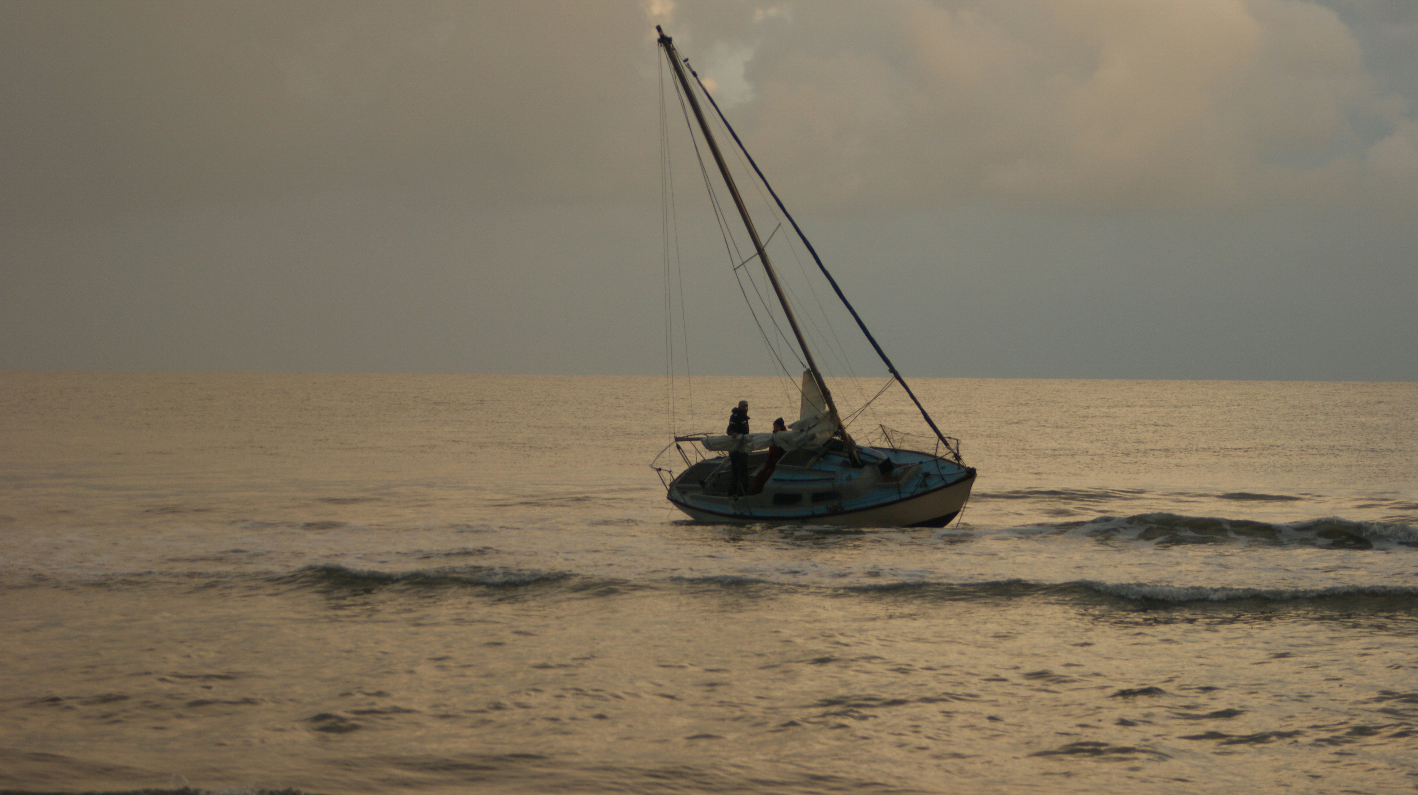 Sailboat gliding through calm waters at dusk, with two figures aboard, surrounded by a tranquil seascape. 