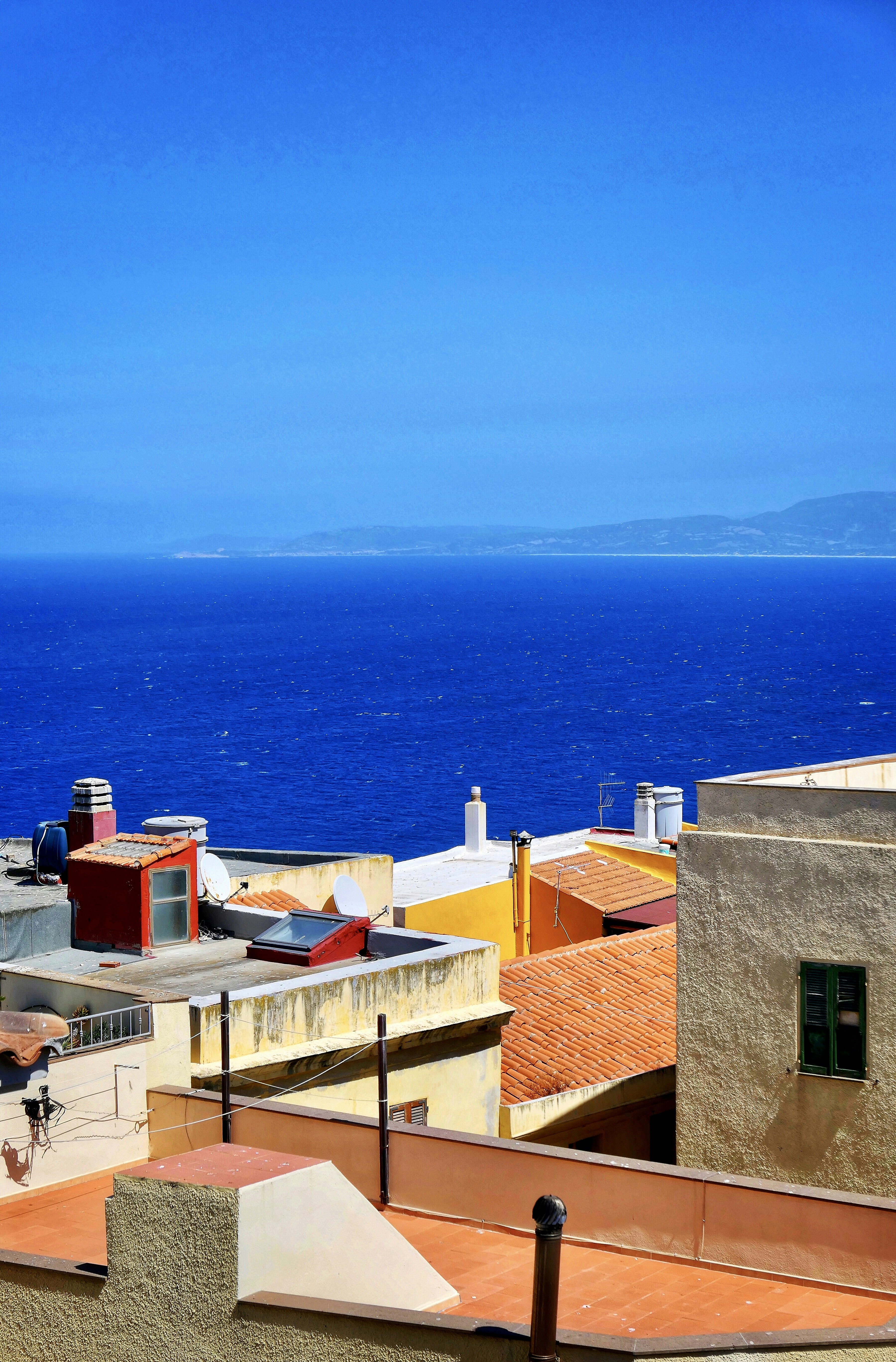 Vibrant rooftops cascade down towards a serene blue sea under a clear sky. The scene captures the essence of coastal living.