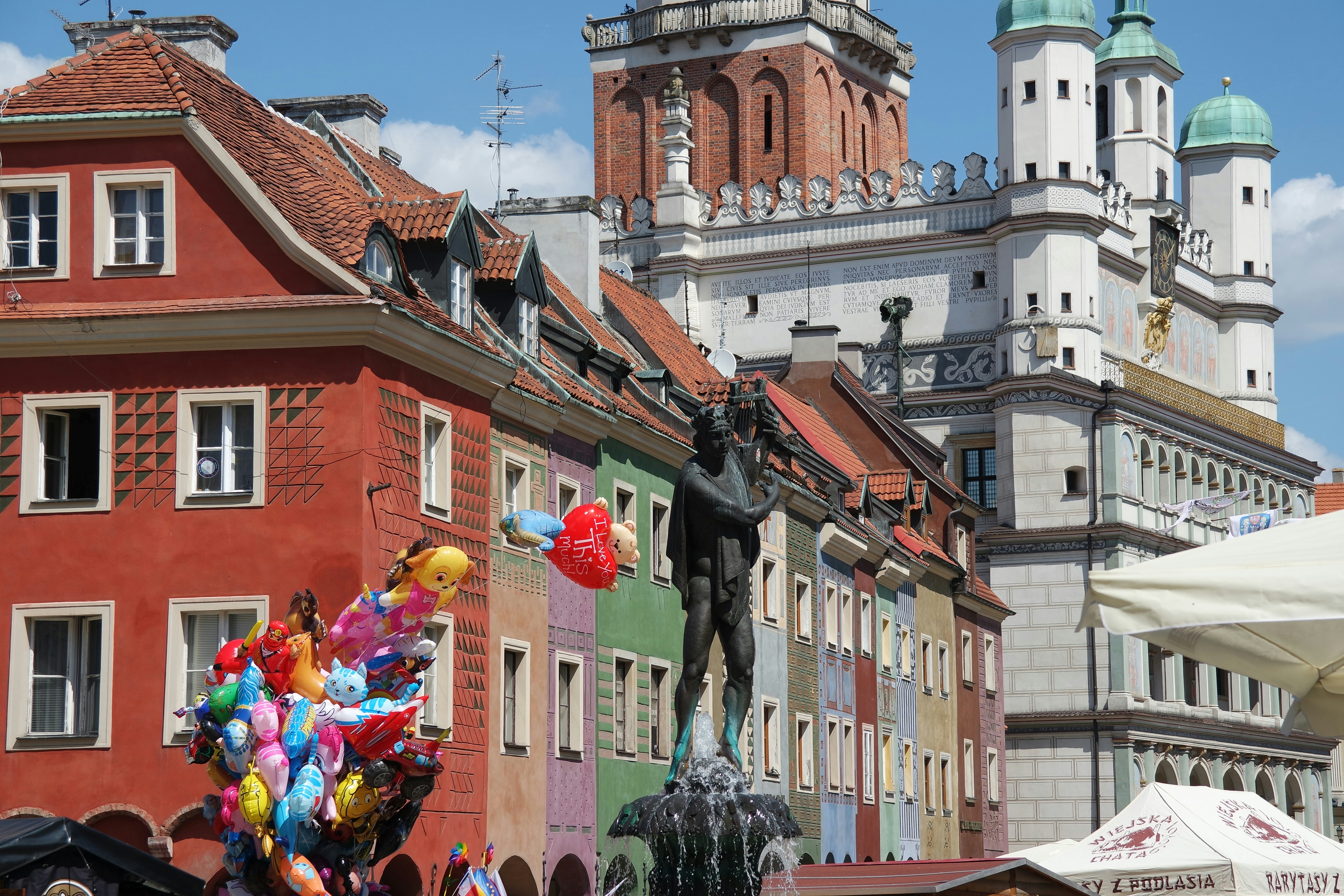 A vibrant fountain statue surrounded by colorful buildings and a cluster of balloons in a lively town square.