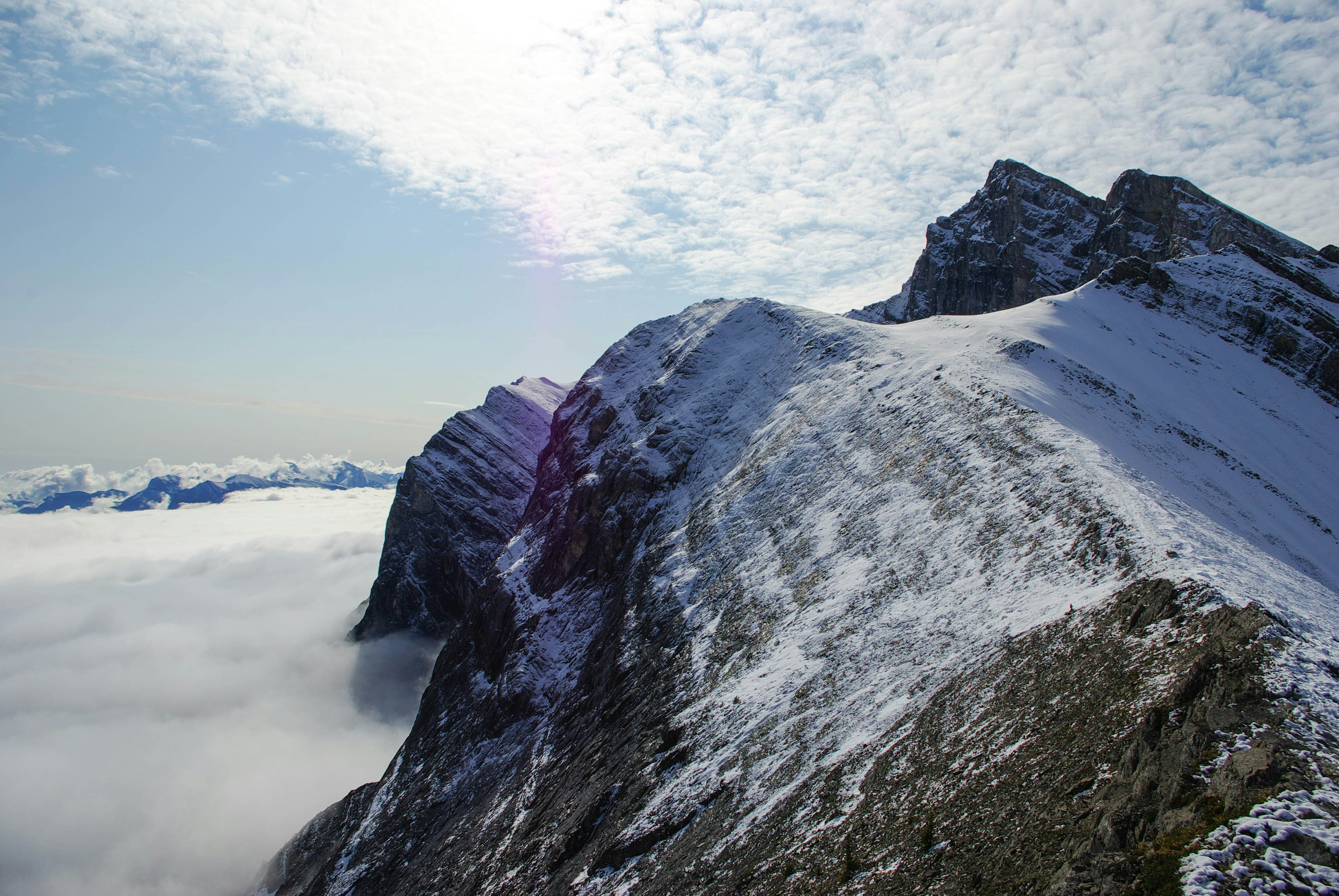 Snow-Capped Ridge Pierces a Sea of Clouds Beneath a Pale Sun