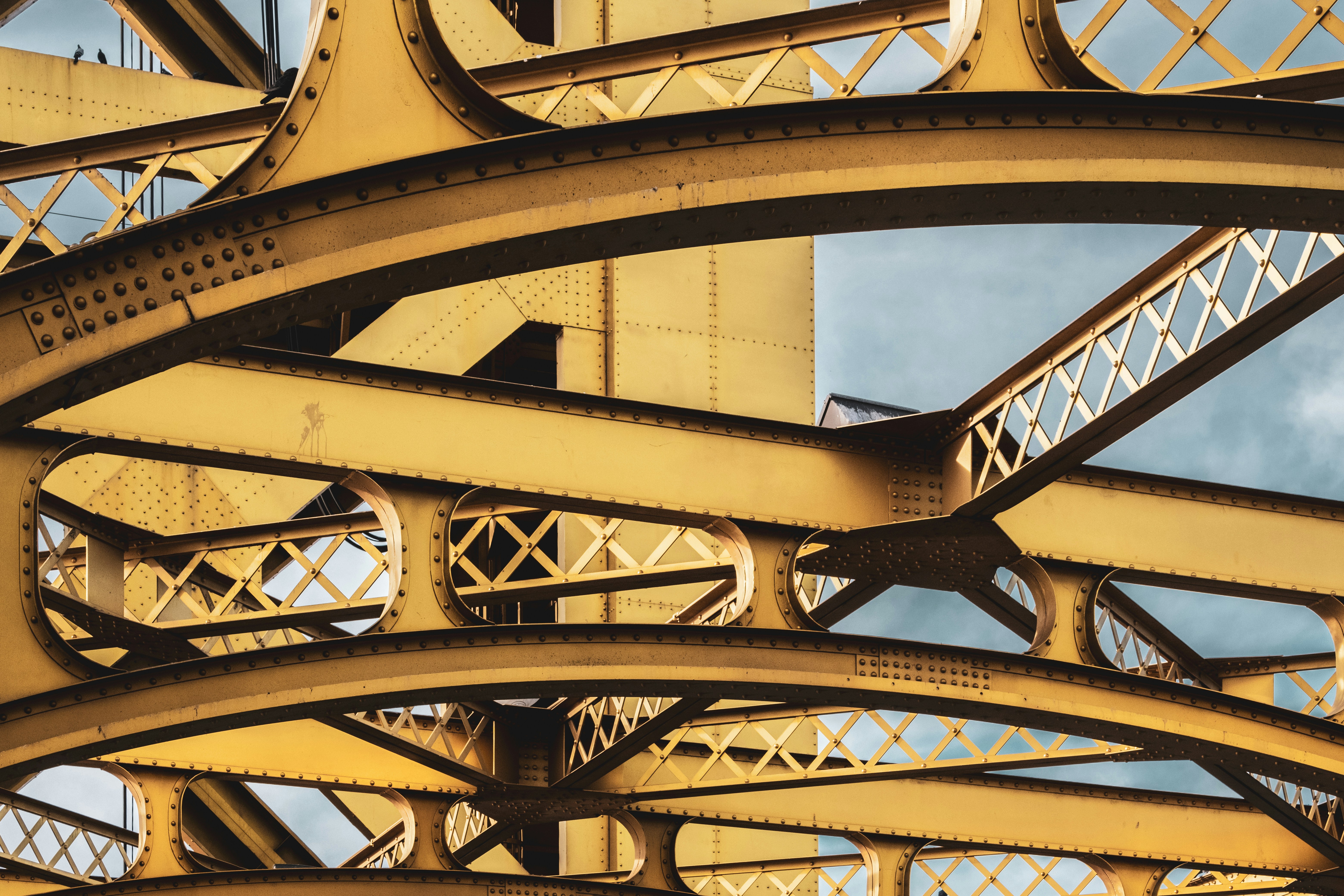 Abstract view of a yellow steel structure showcasing intricate patterns and lines against a cloudy sky.
