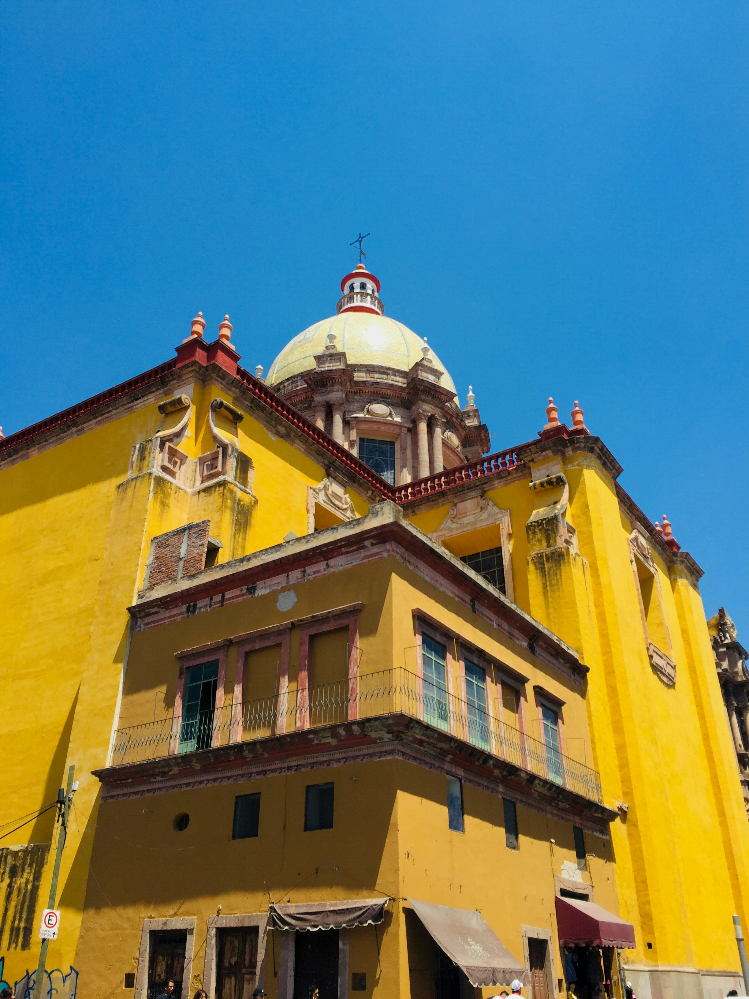 Bright yellow building with intricate architectural details and a prominent dome under a clear blue sky.