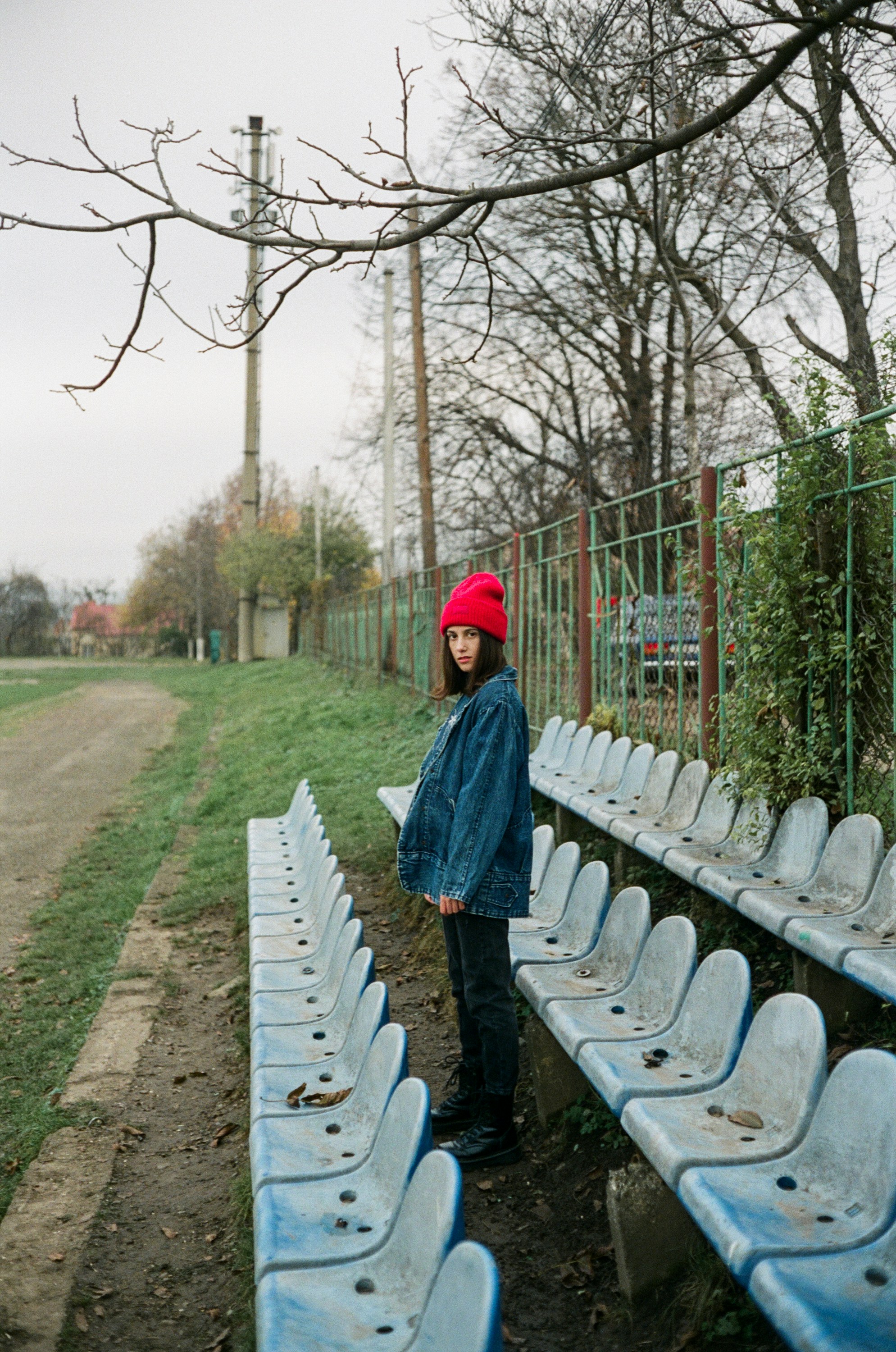 Red Beanie, Green Fence: A Quiet Moment on the Bleachers