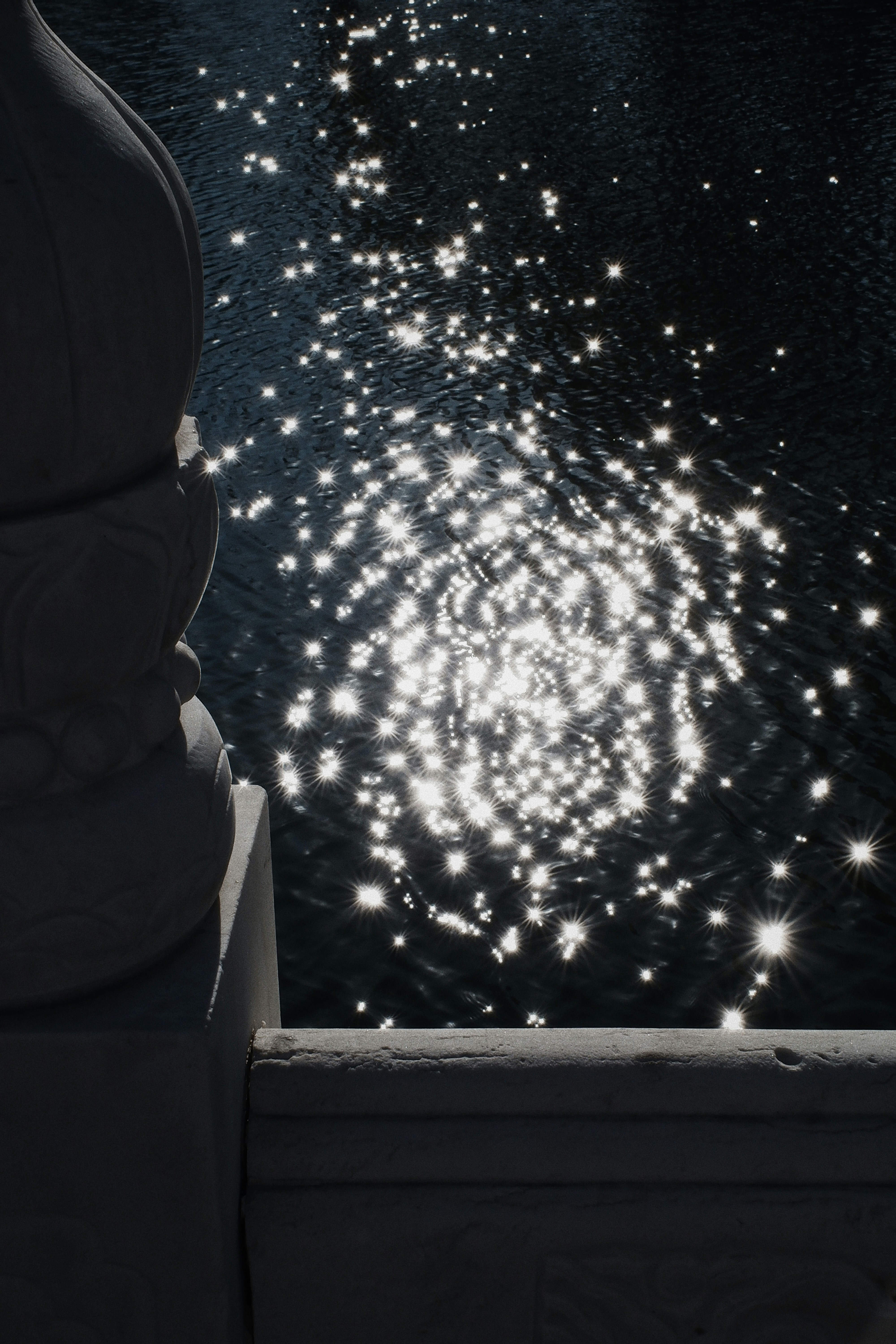 Sparkling reflections on a tranquil water surface, framed by a decorative stone edge.