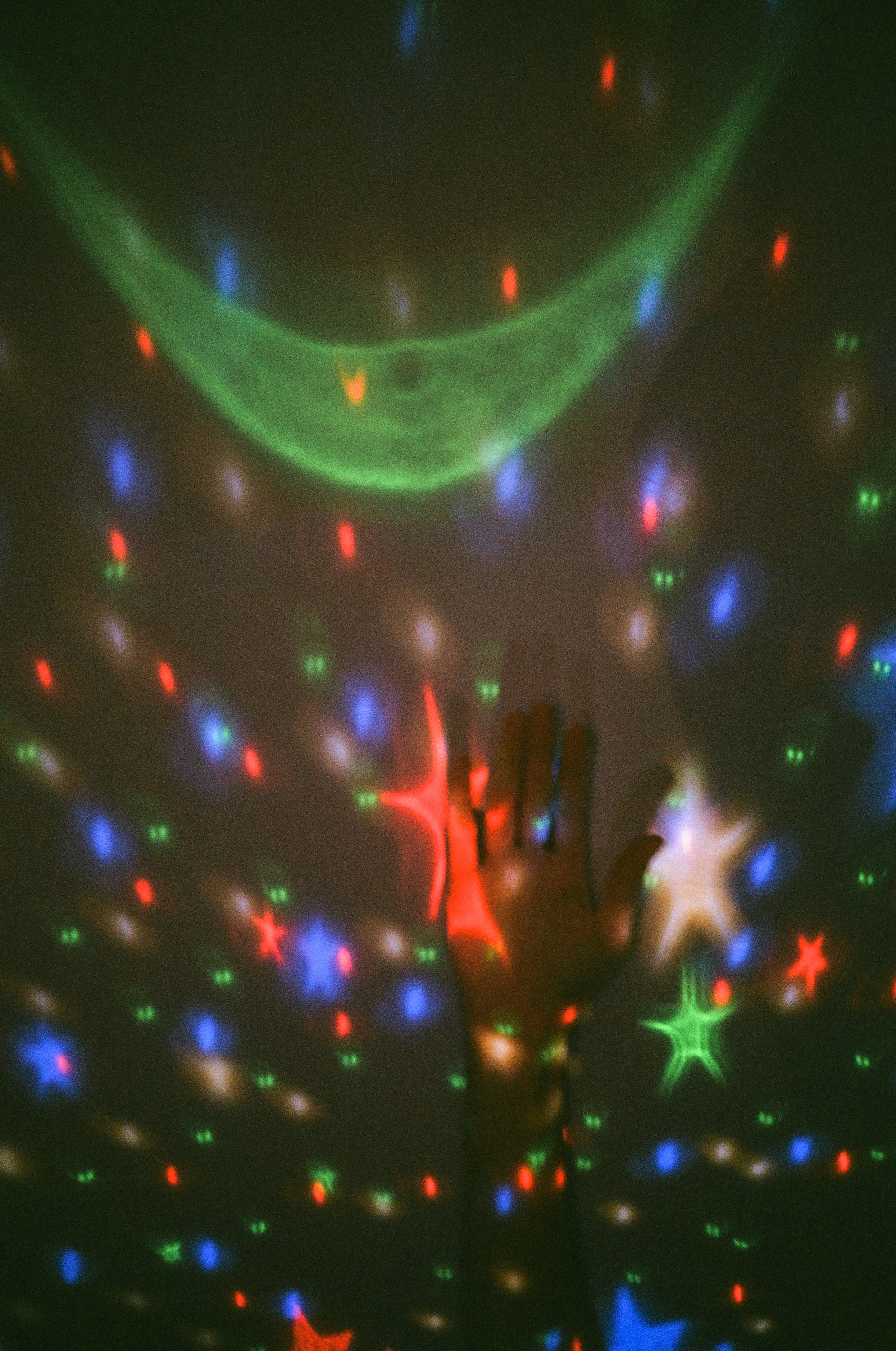 Raised hand silhouette amid a field of multicolored star-like projections from a light projector.