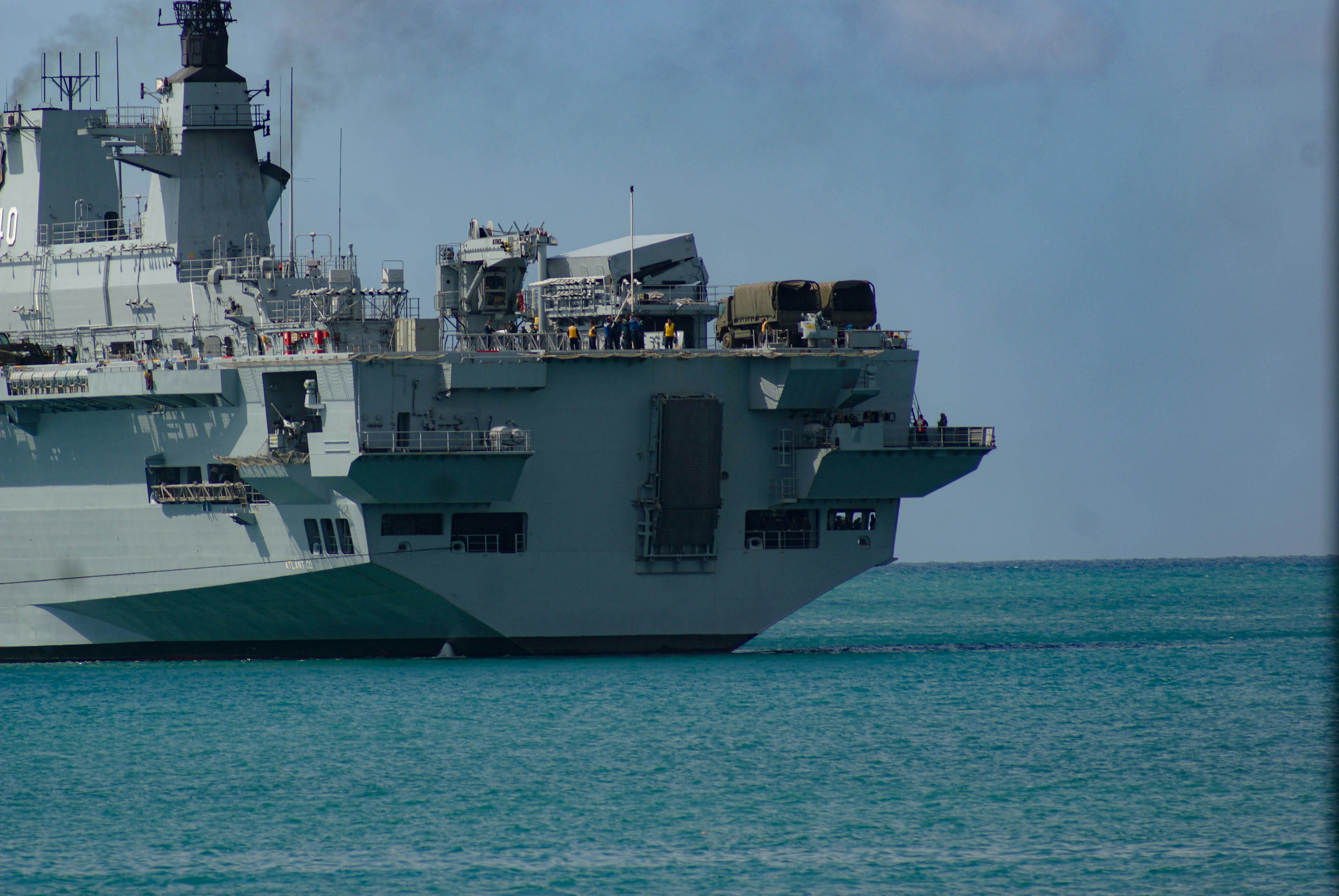 Large naval ship anchored in calm, blue-green ocean with a clear sky.