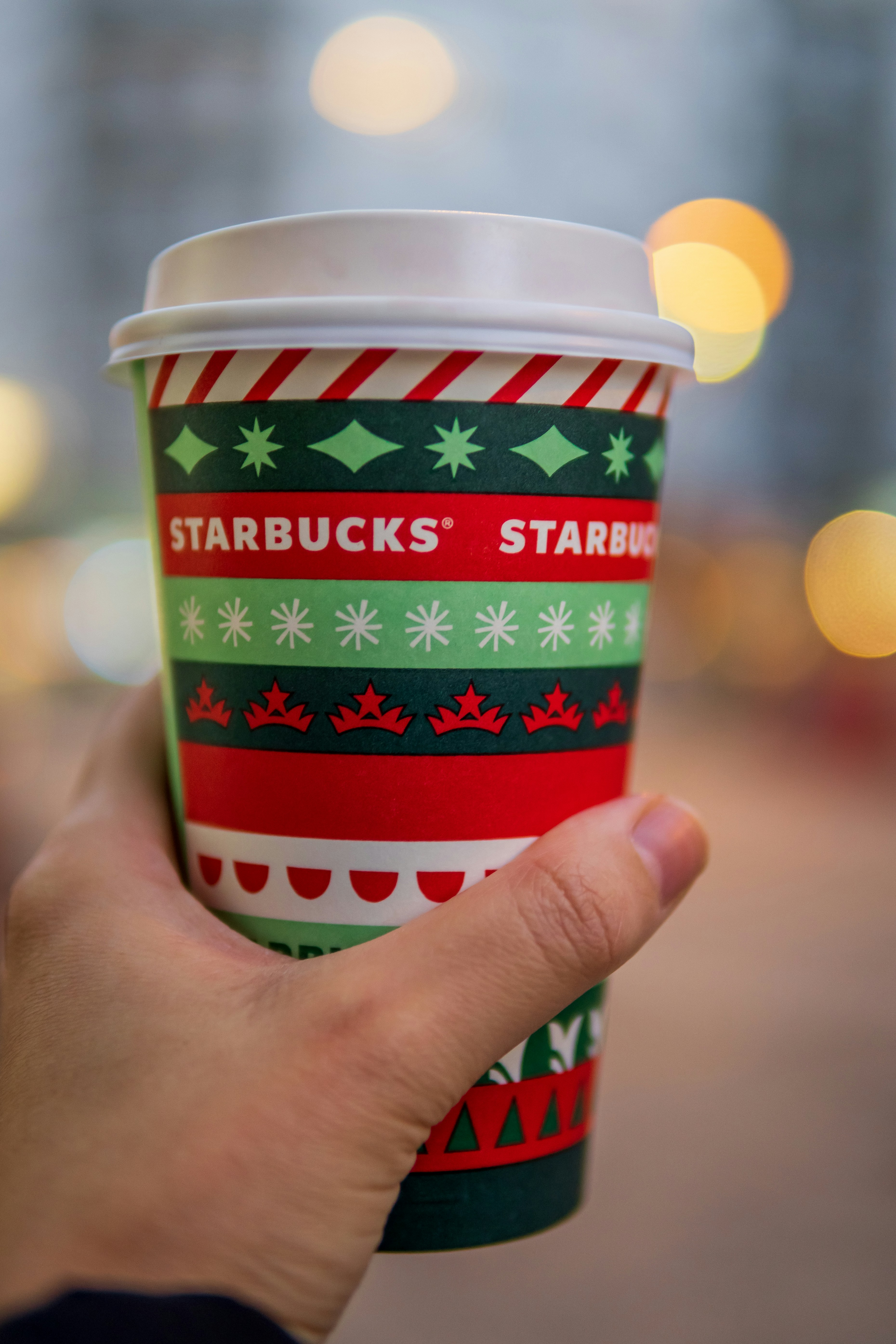 Holiday Cheer in Hand: A Starbucks Cup Framed by City Lights