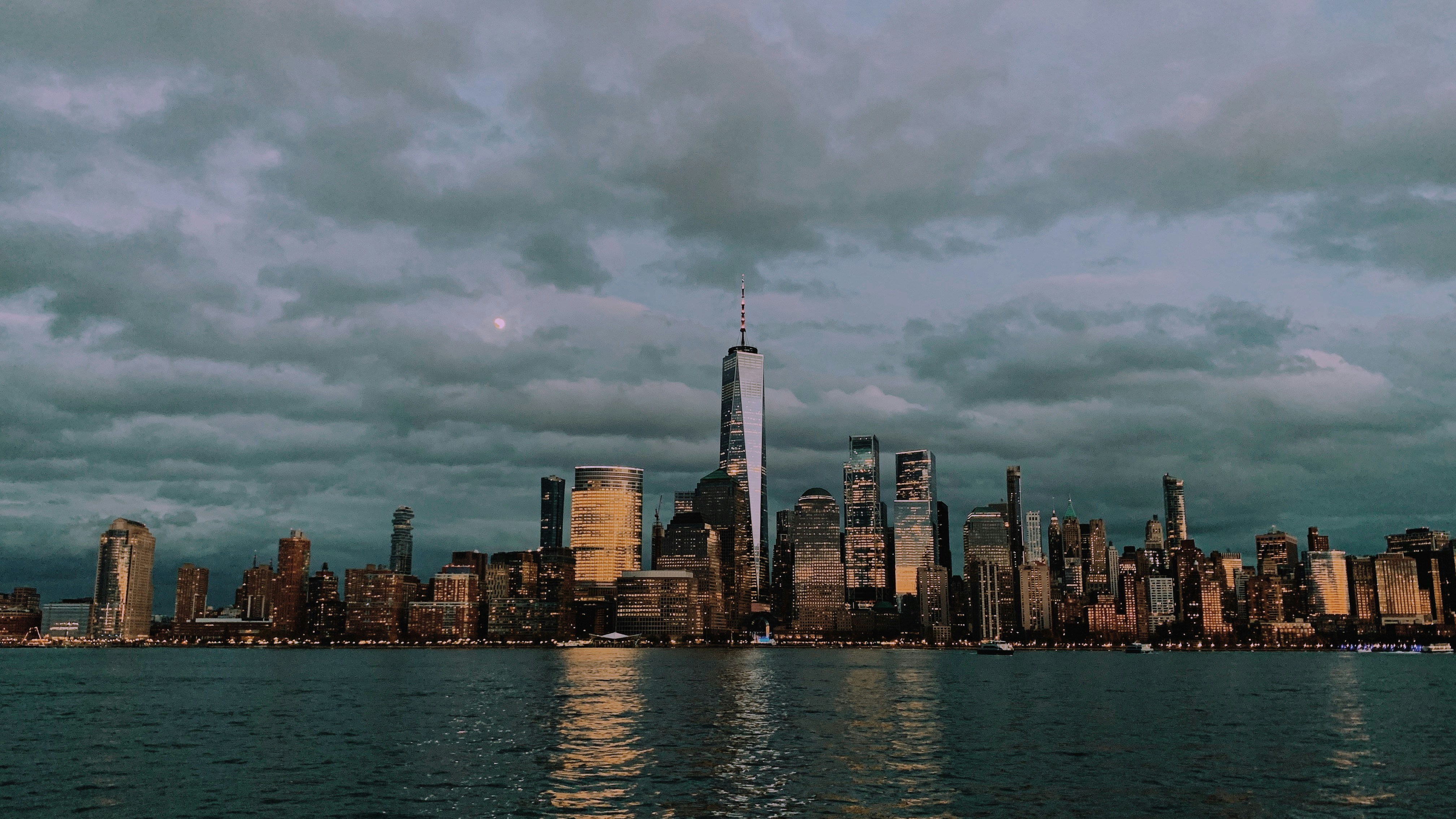 City skyline mirrored in calm water under a cloudy sky.