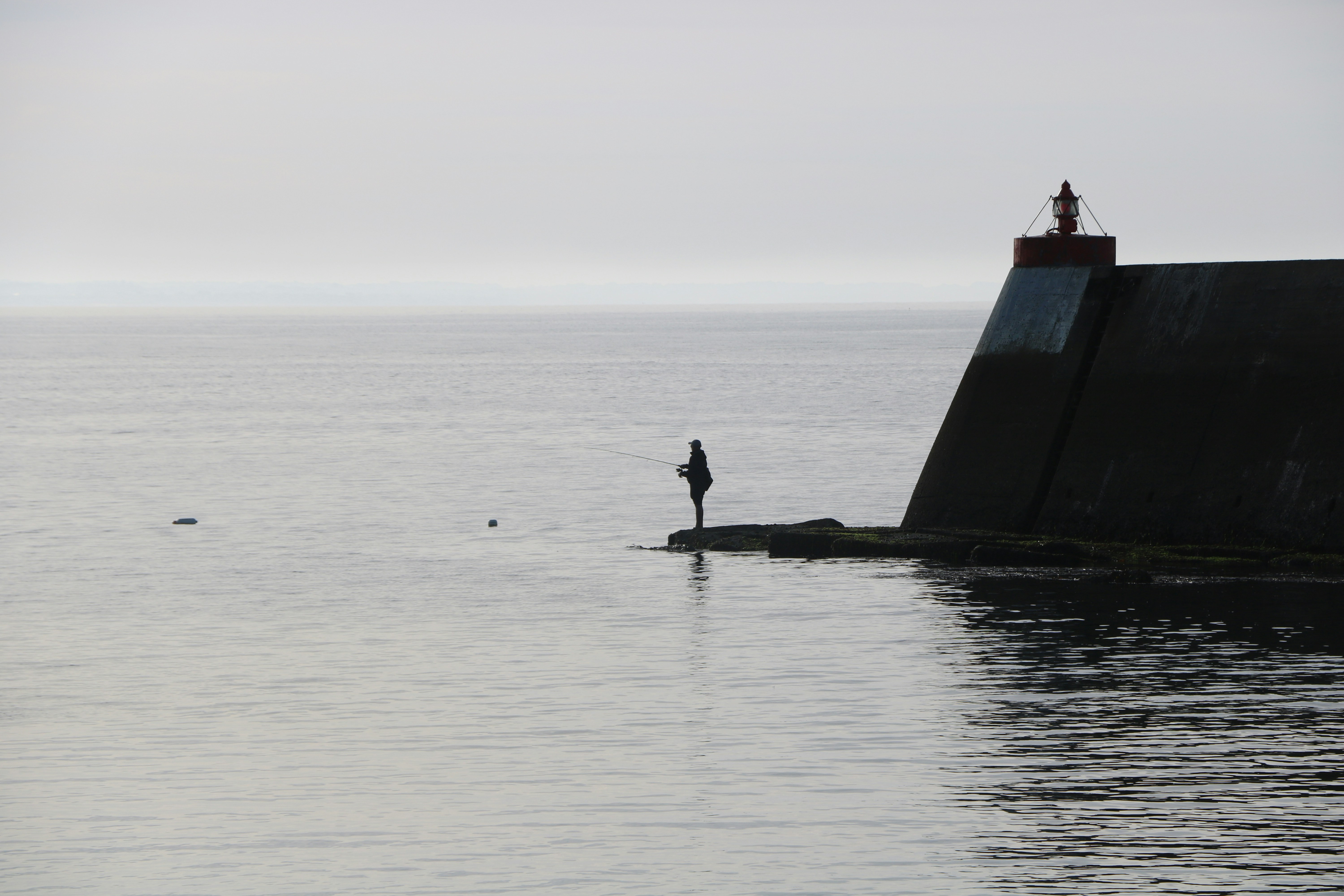 silhouette of person sitting on rock in the middle of the sea