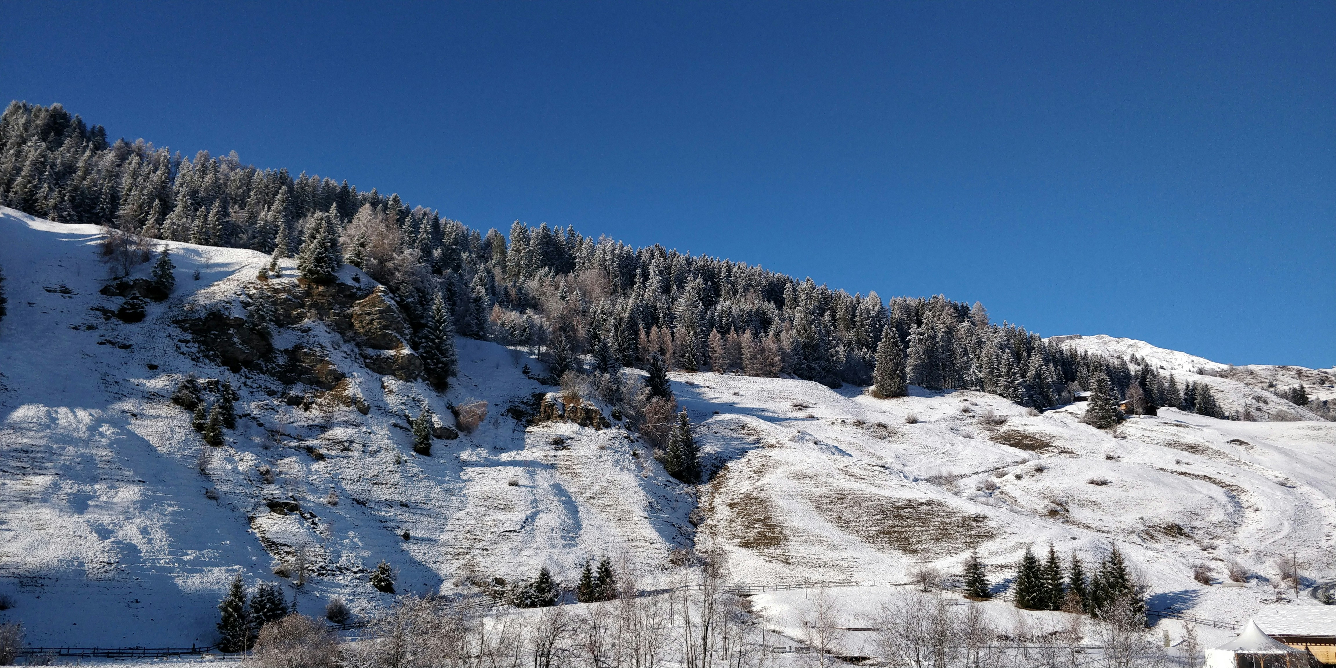 Snow-laden slopes and frosted trees create a serene alpine scene under a clear blue sky.