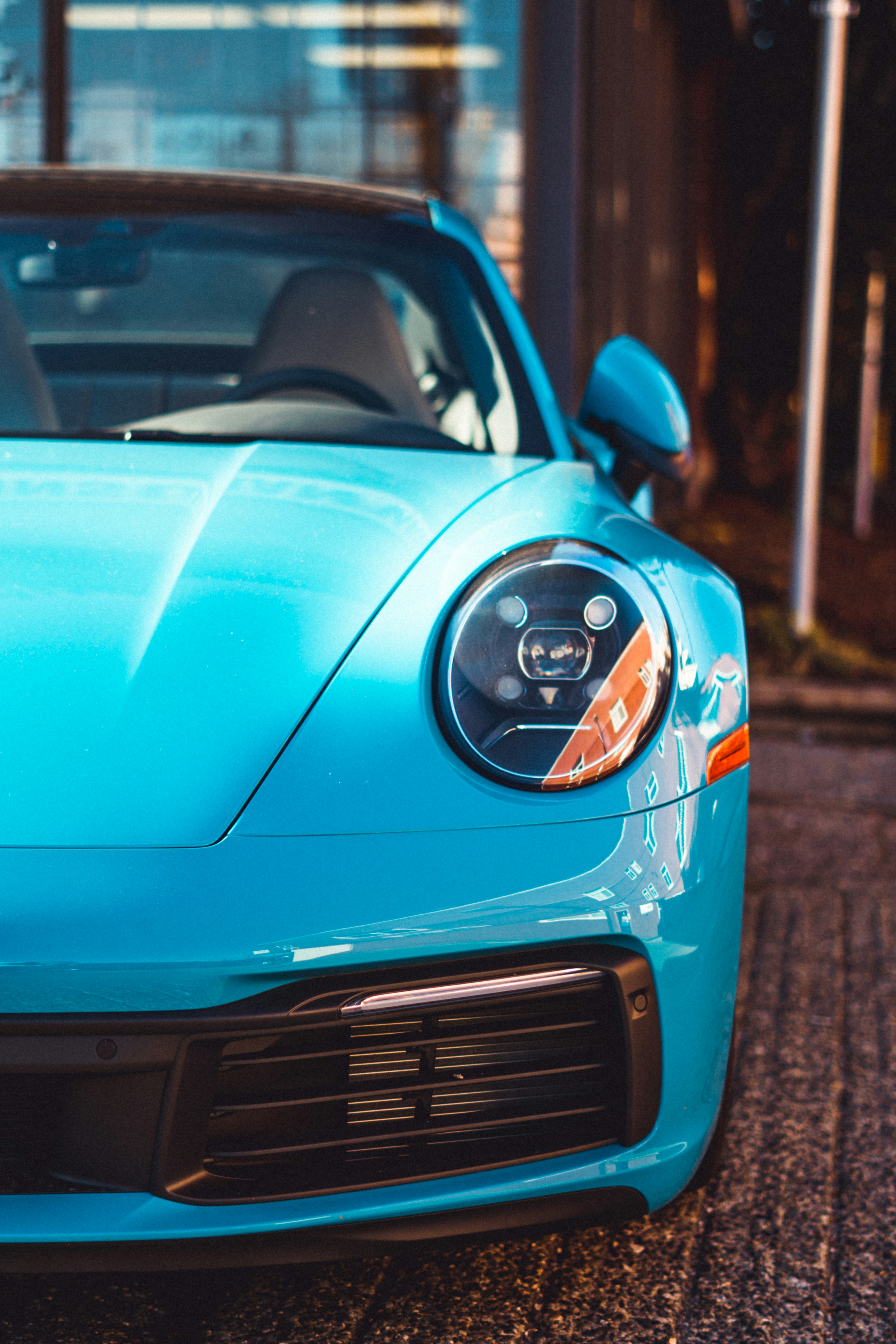 Close-up of a sleek aqua sports car showcasing its distinctive headlight and streamlined design. The vibrant color contrasts with the urban backdrop.