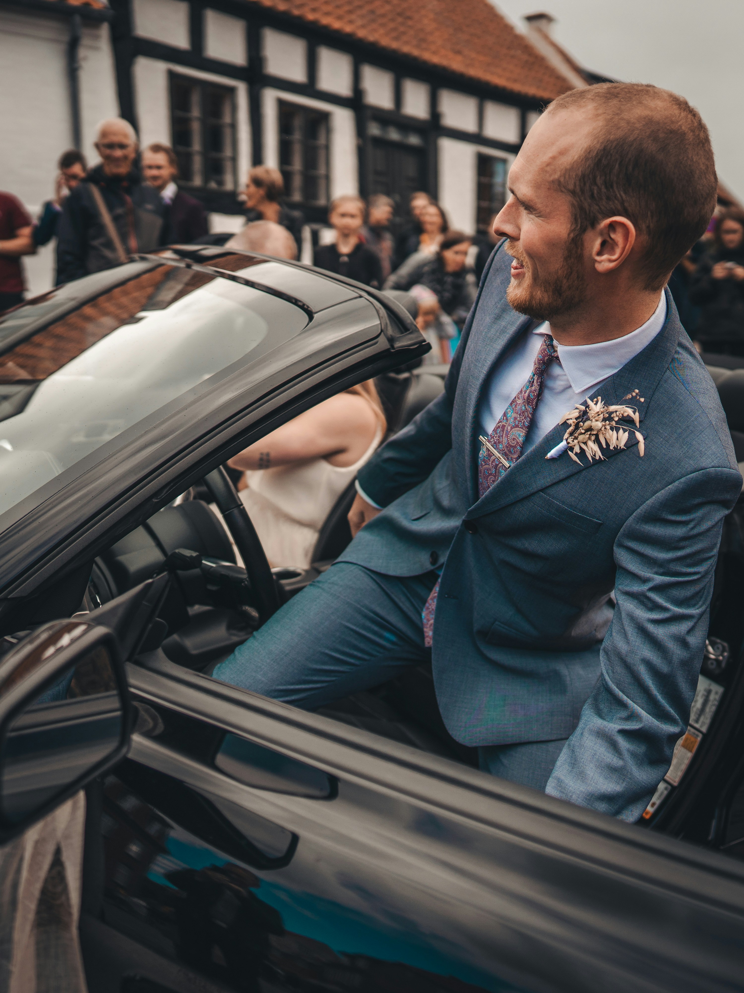 Blue-Toned Entrance: A Groom Steps from a Glossy Convertible at a Wedding