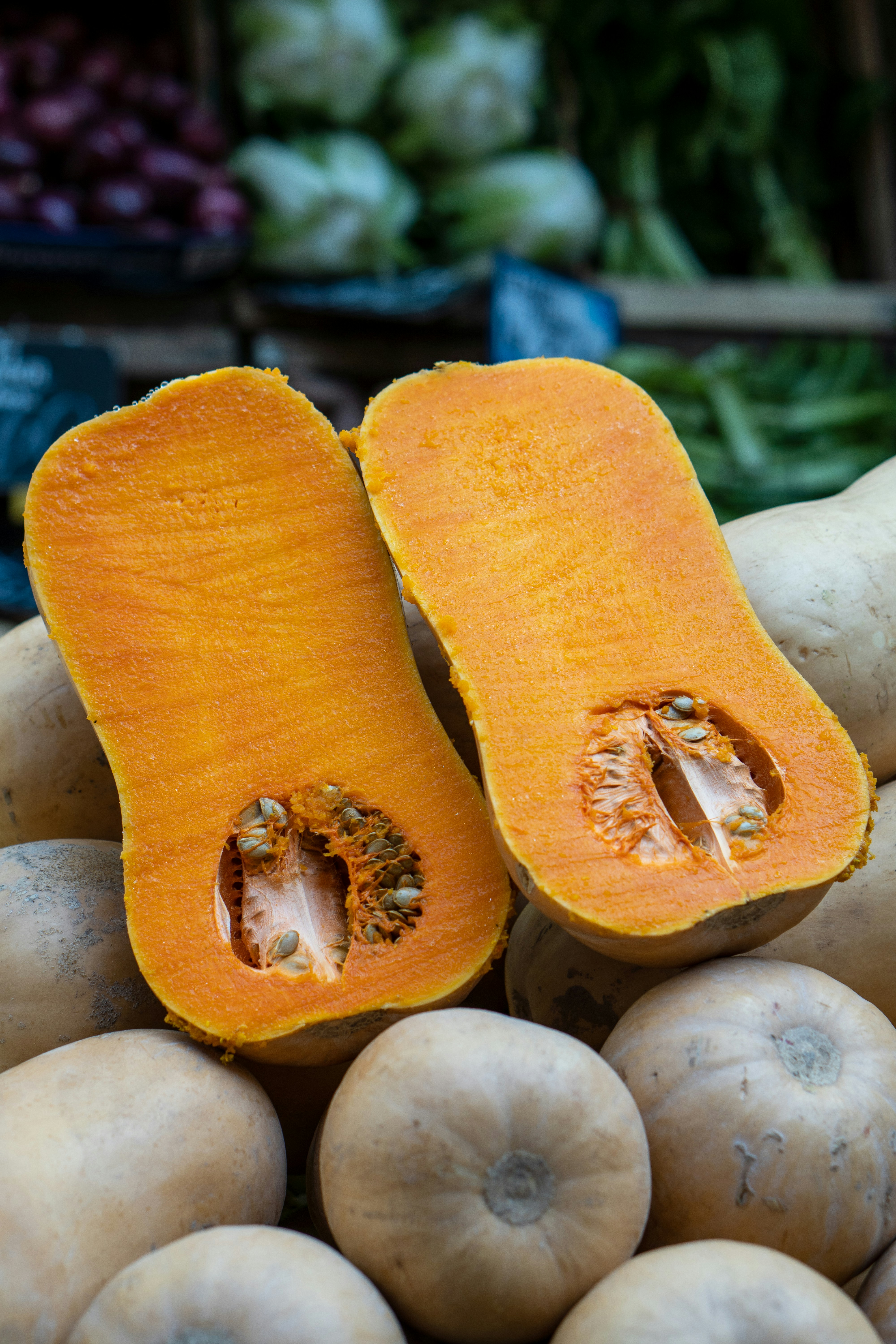 Halved butternut squash showcasing vibrant orange flesh and seeds, surrounded by whole squashes at a market stall.
