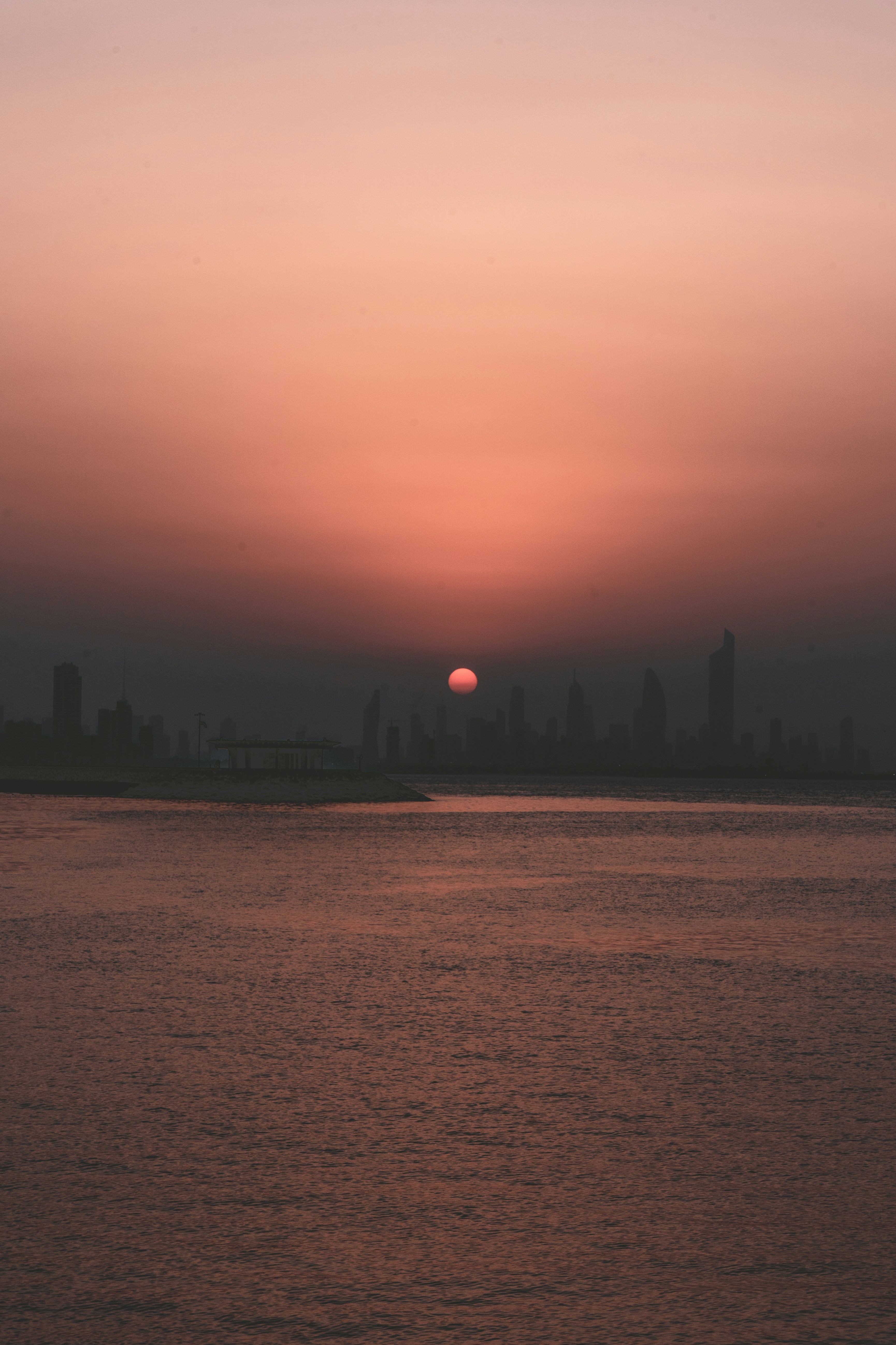 Silhouette of a city skyline against a glowing sunset, reflecting warm hues on the water's surface.