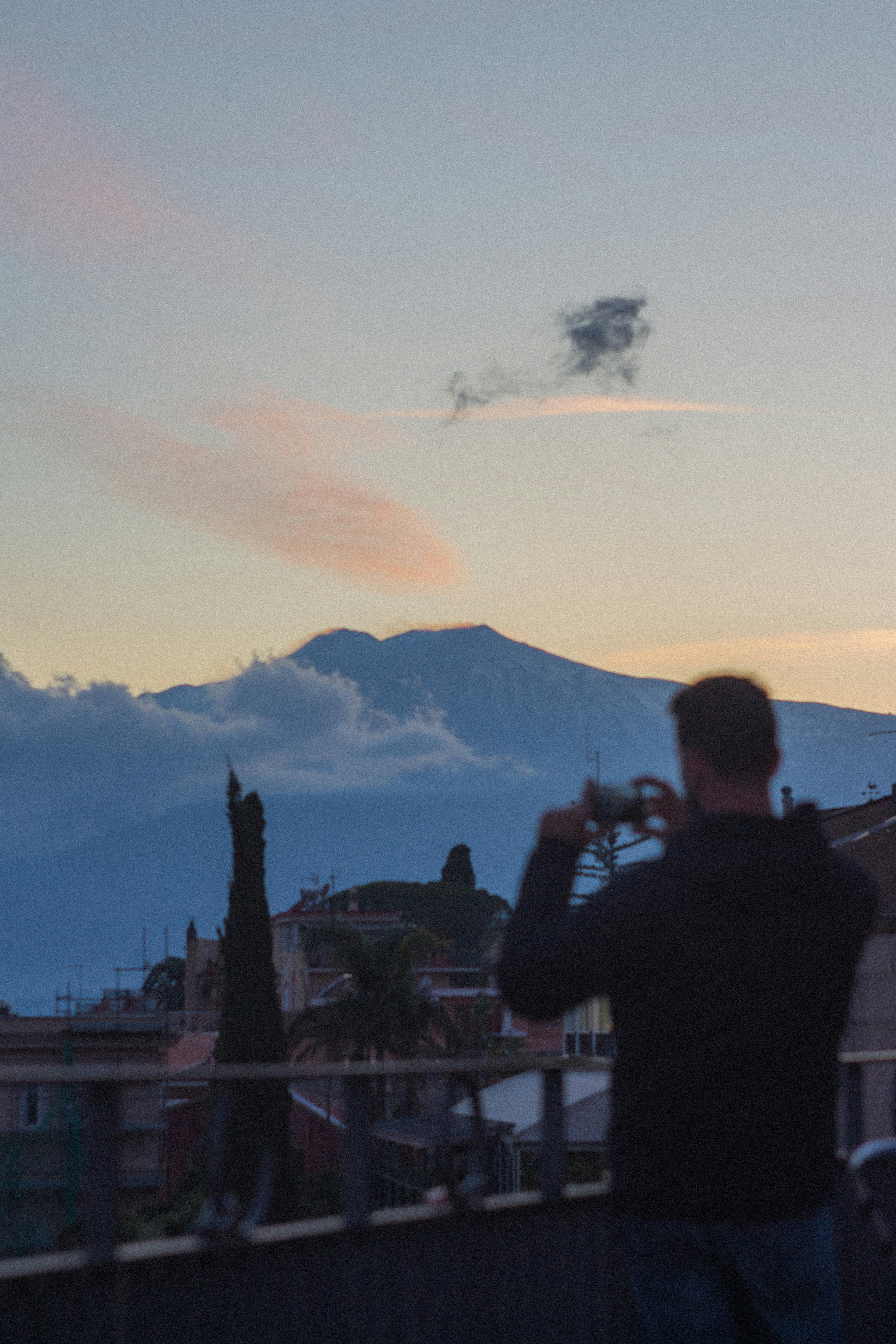 Silhouette of a person photographing a mountain at dusk with pastel skies.