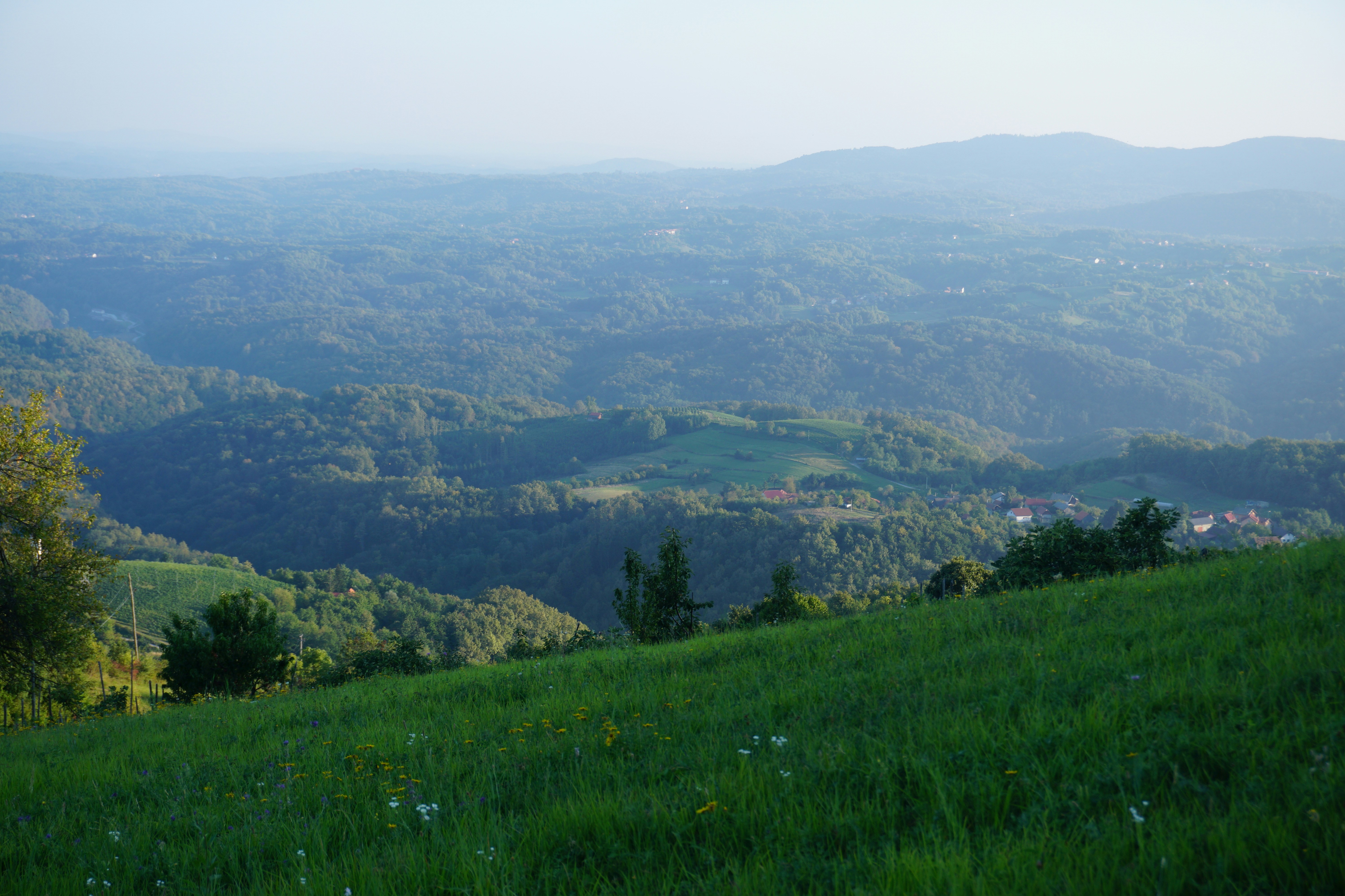 Lush green hills and valleys stretch into the distance, framed by a gentle blue sky, highlighting the serene beauty of the landscape.
