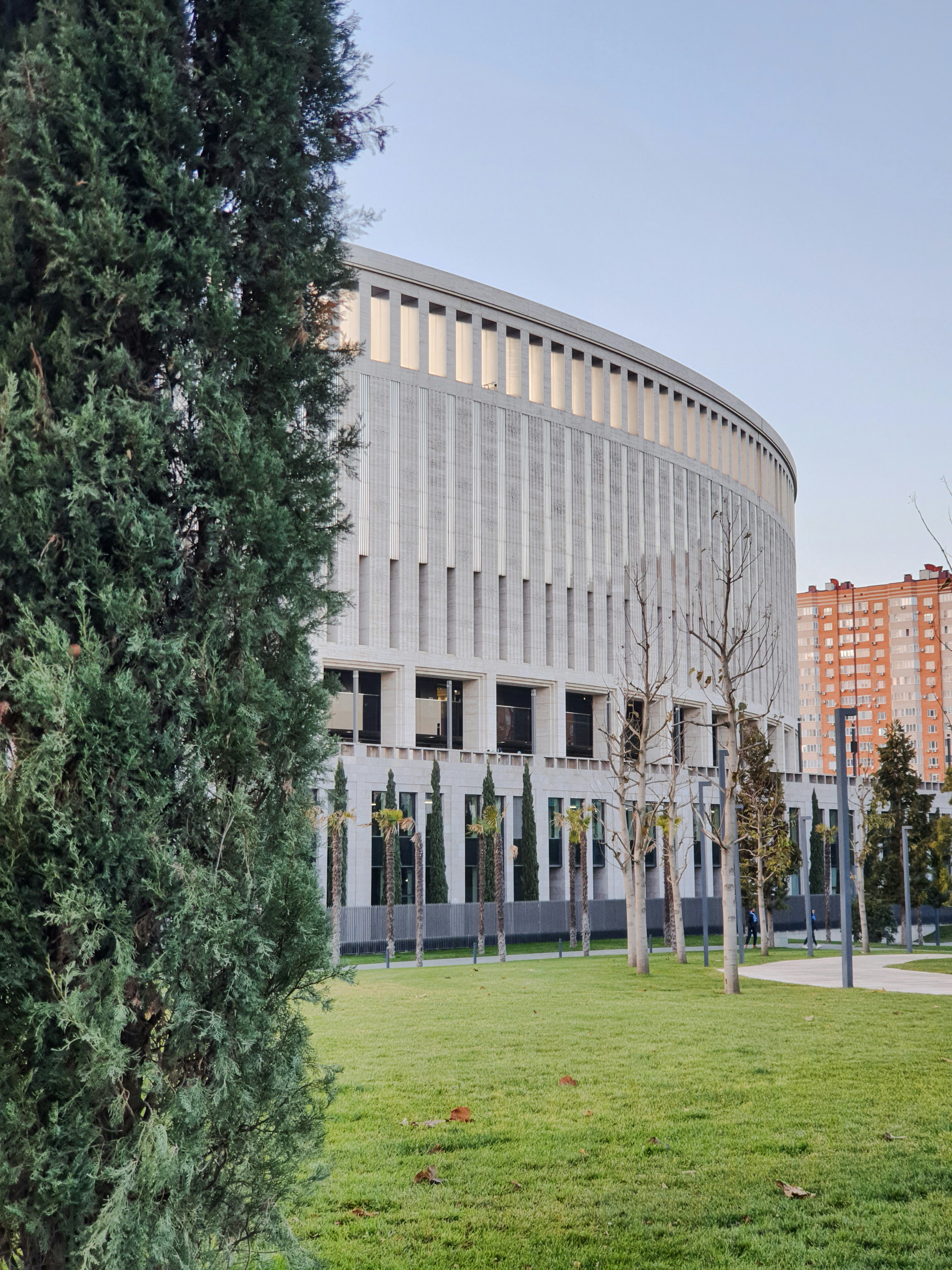Curved modern building framed by lush greenery and a clear sky, showcasing a blend of architecture and nature.