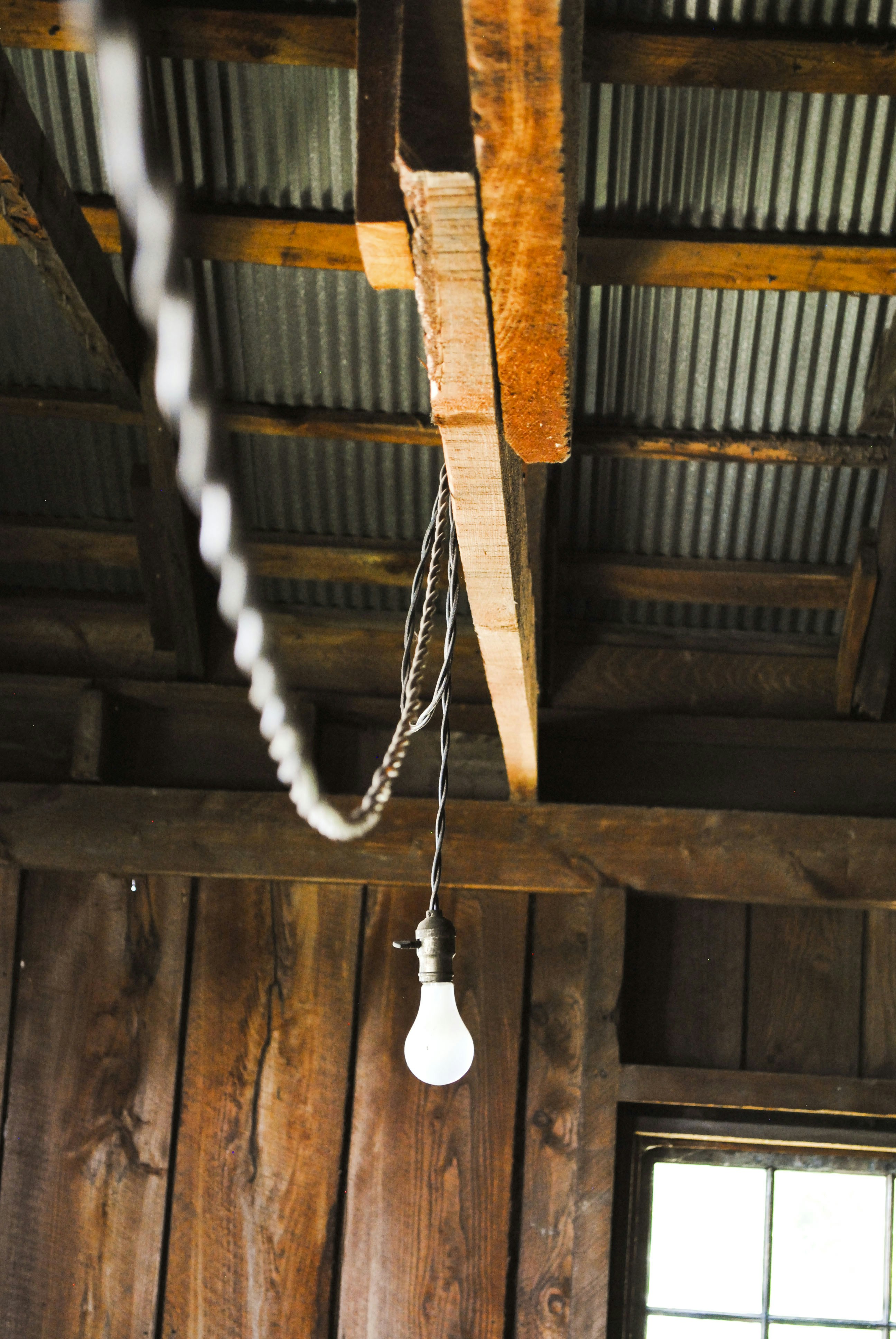 Bare light bulb hanging from a wooden beam in a rustic interior, showcasing the charm of a simple, unadorned space.