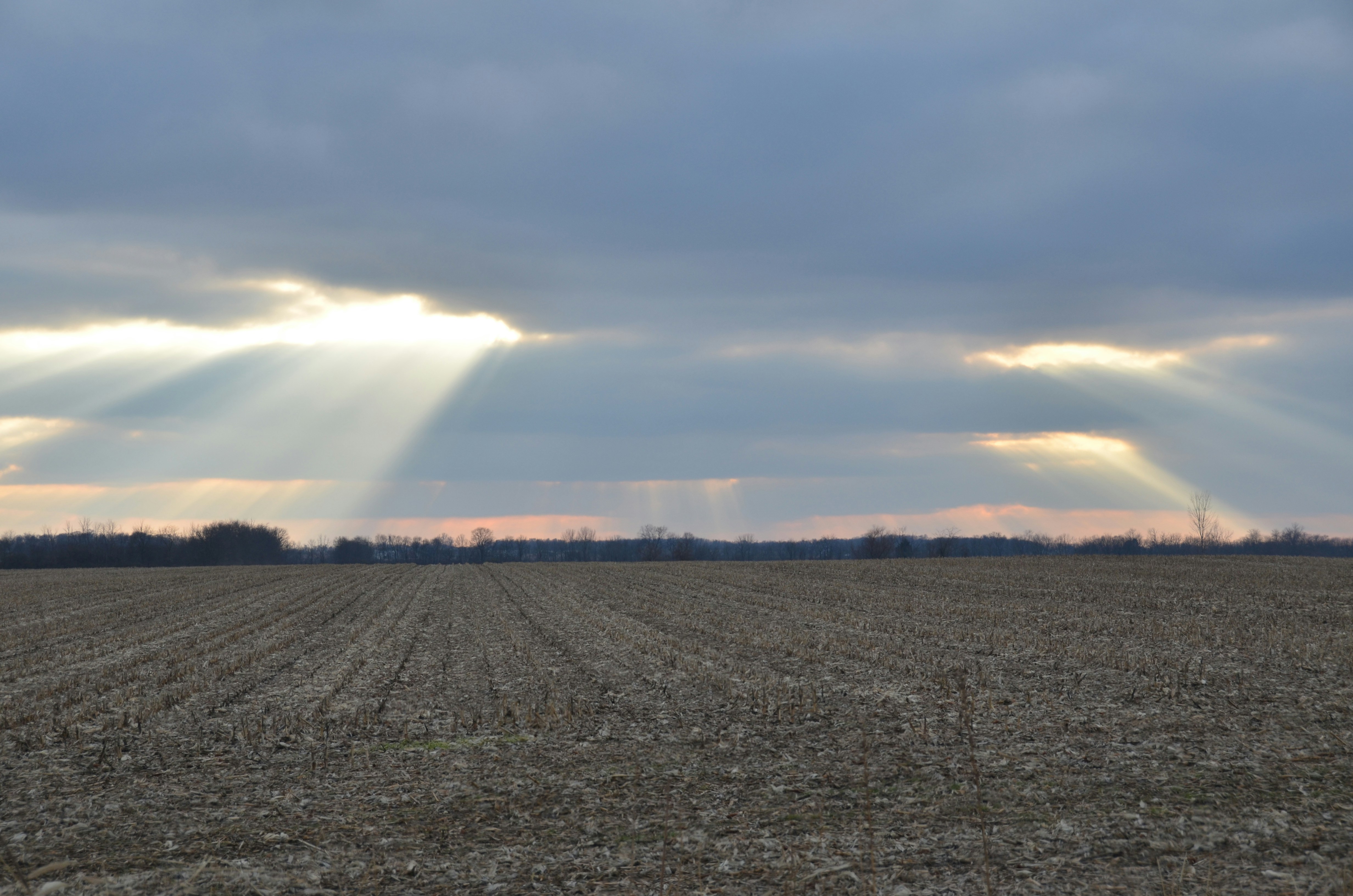 Sunbeams Split the Cloudy Sky Over a Quiet Plowed Field