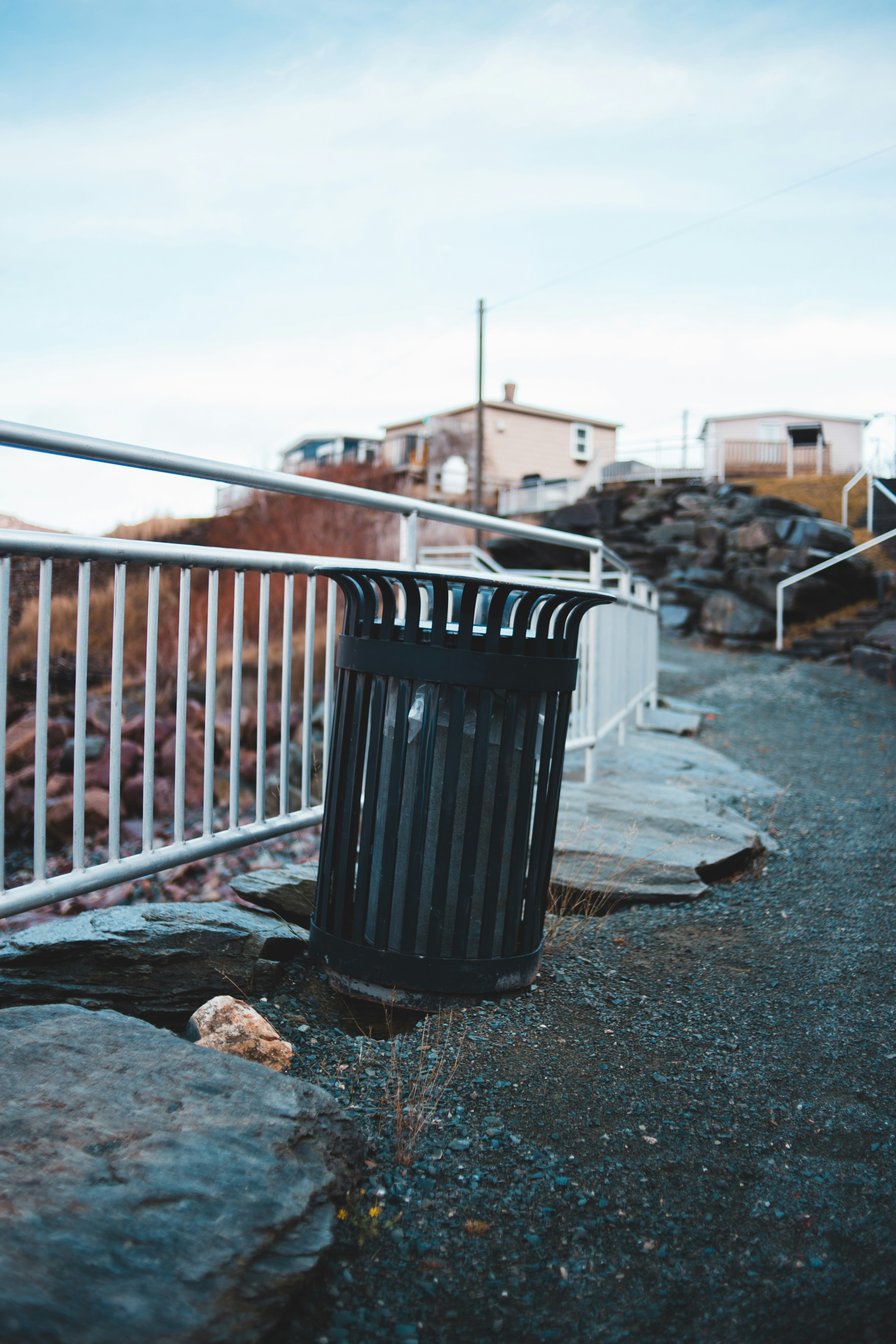 Coastal Corridor: A Black Metal Trash Can Framed by Rails and Rocks