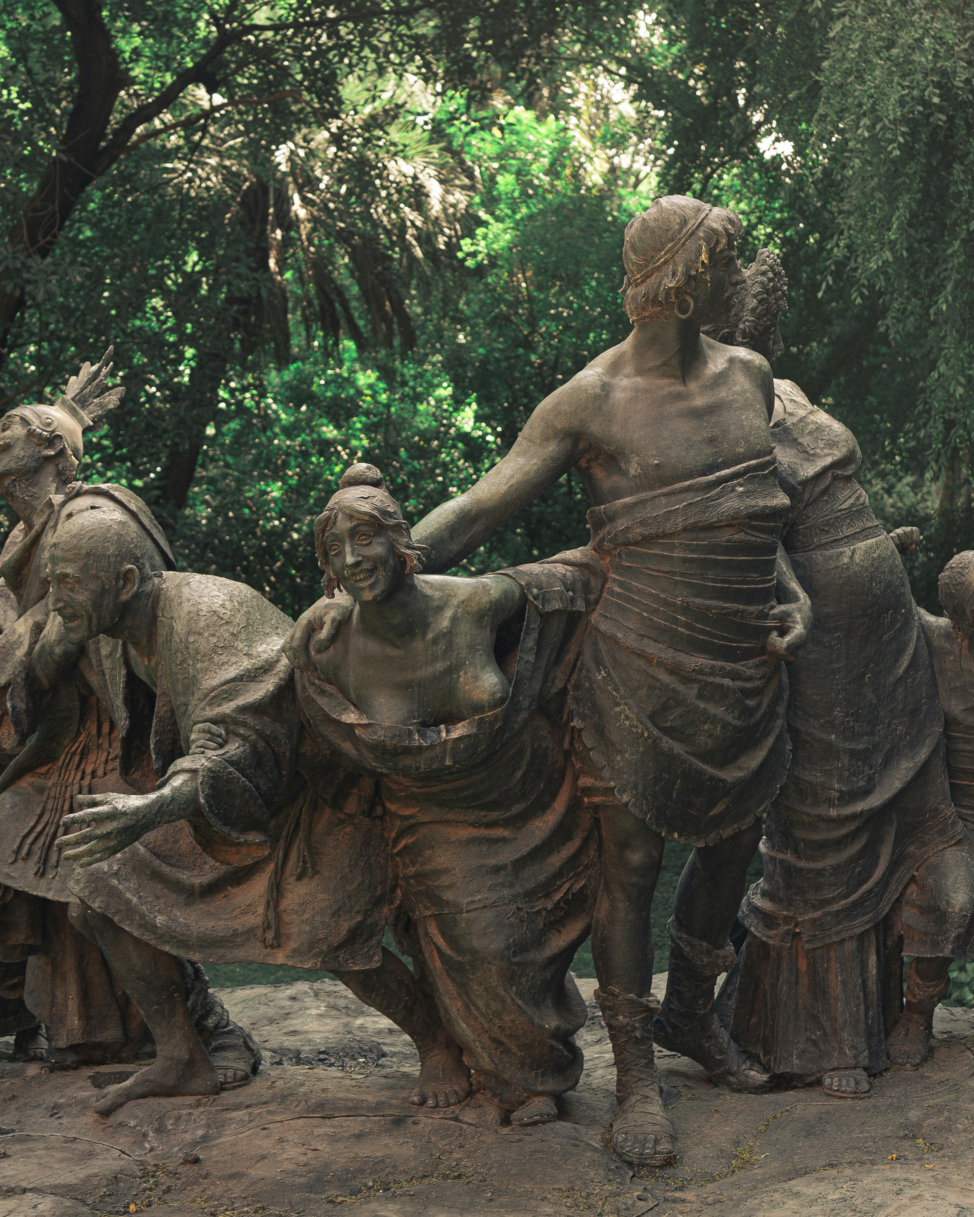A group of intricately detailed sculptures depicting figures in dynamic poses, surrounded by lush greenery. The artwork captures a moment of movement and emotion.
