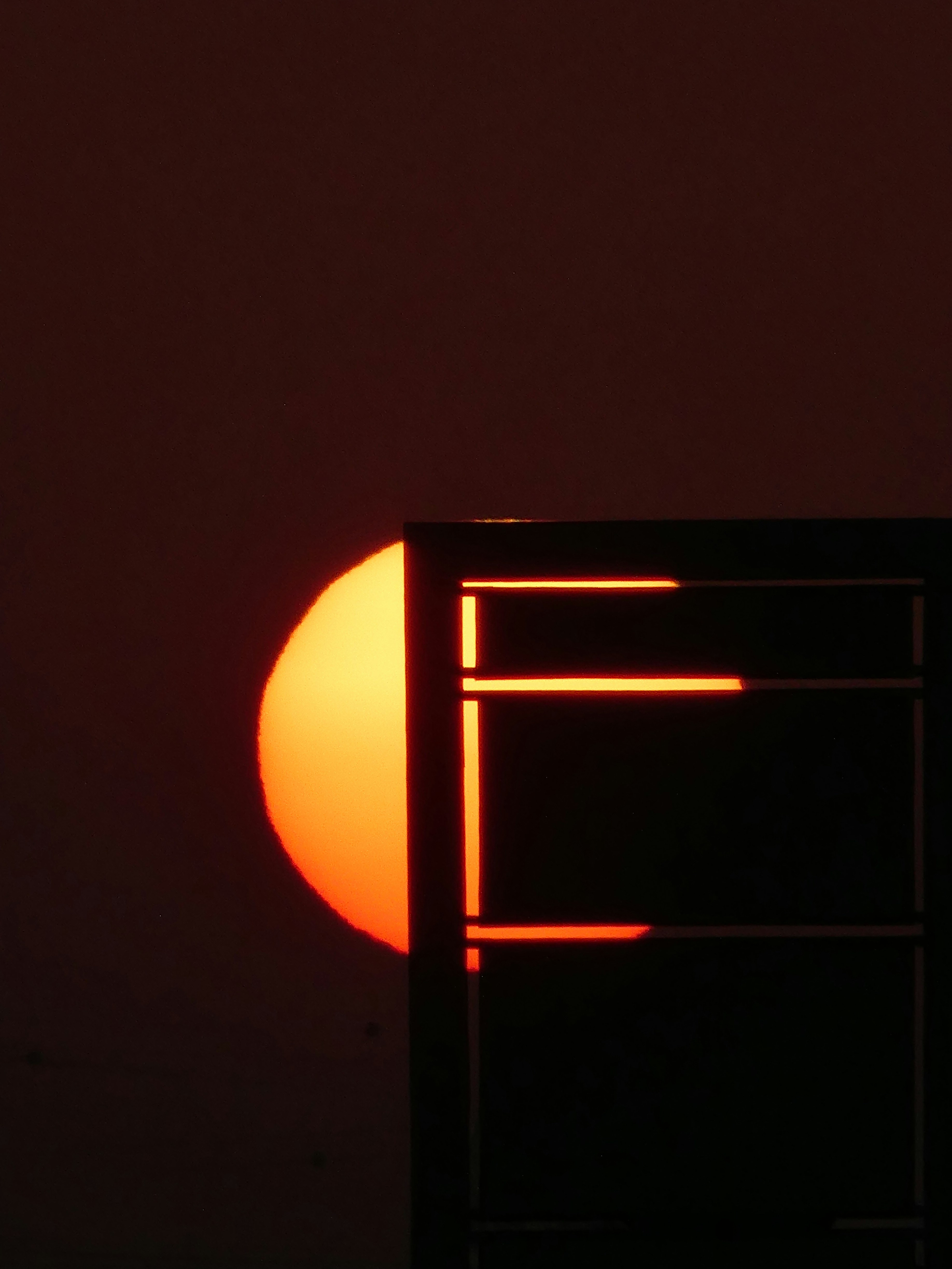 The sun emerges behind a dark silhouette, casting a warm glow against a gradient sky. This striking composition emphasizes the contrast between light and shadow.