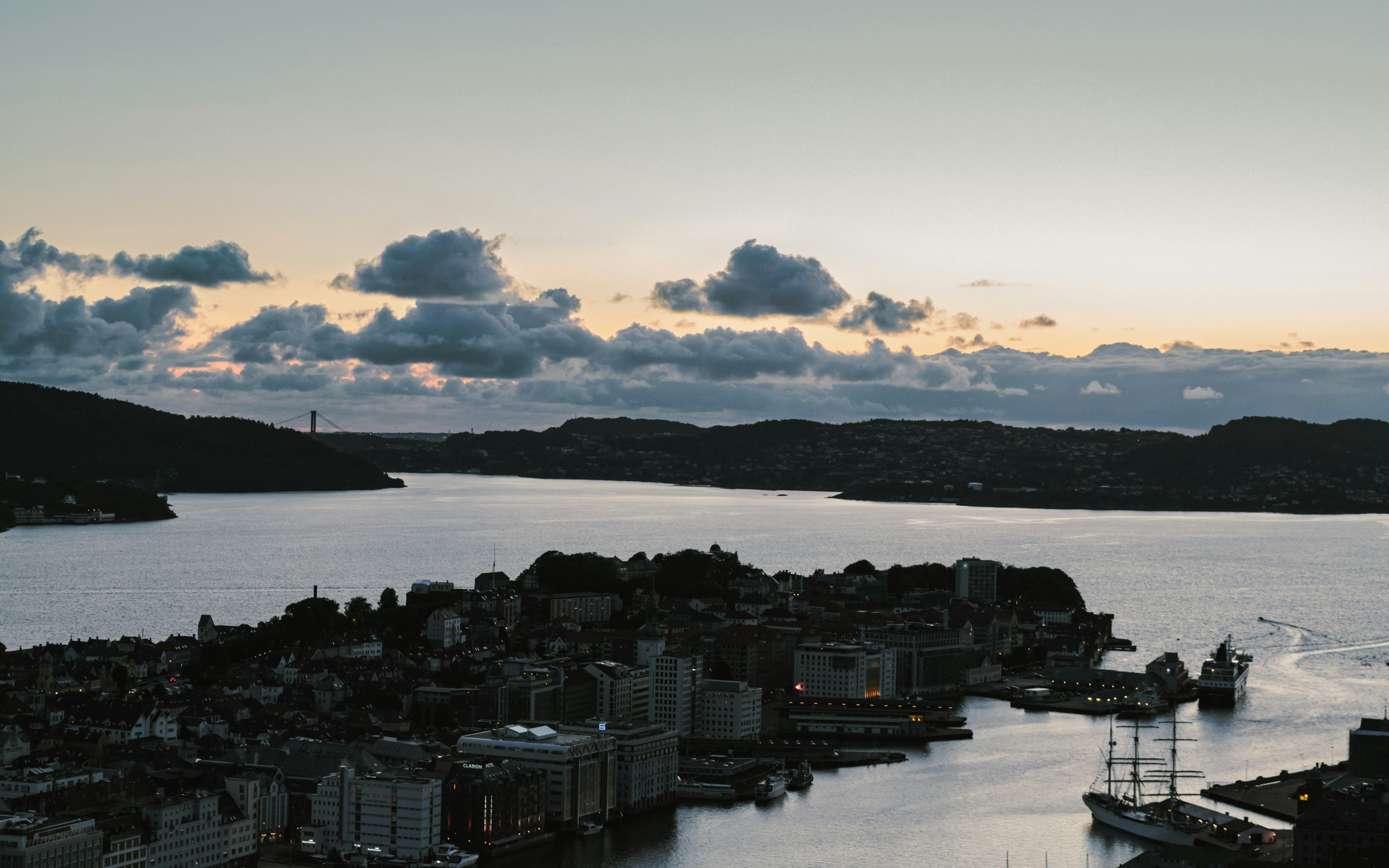 Cityscape of Bergen at dusk with silhouetted buildings and calm water reflecting the fading light.
