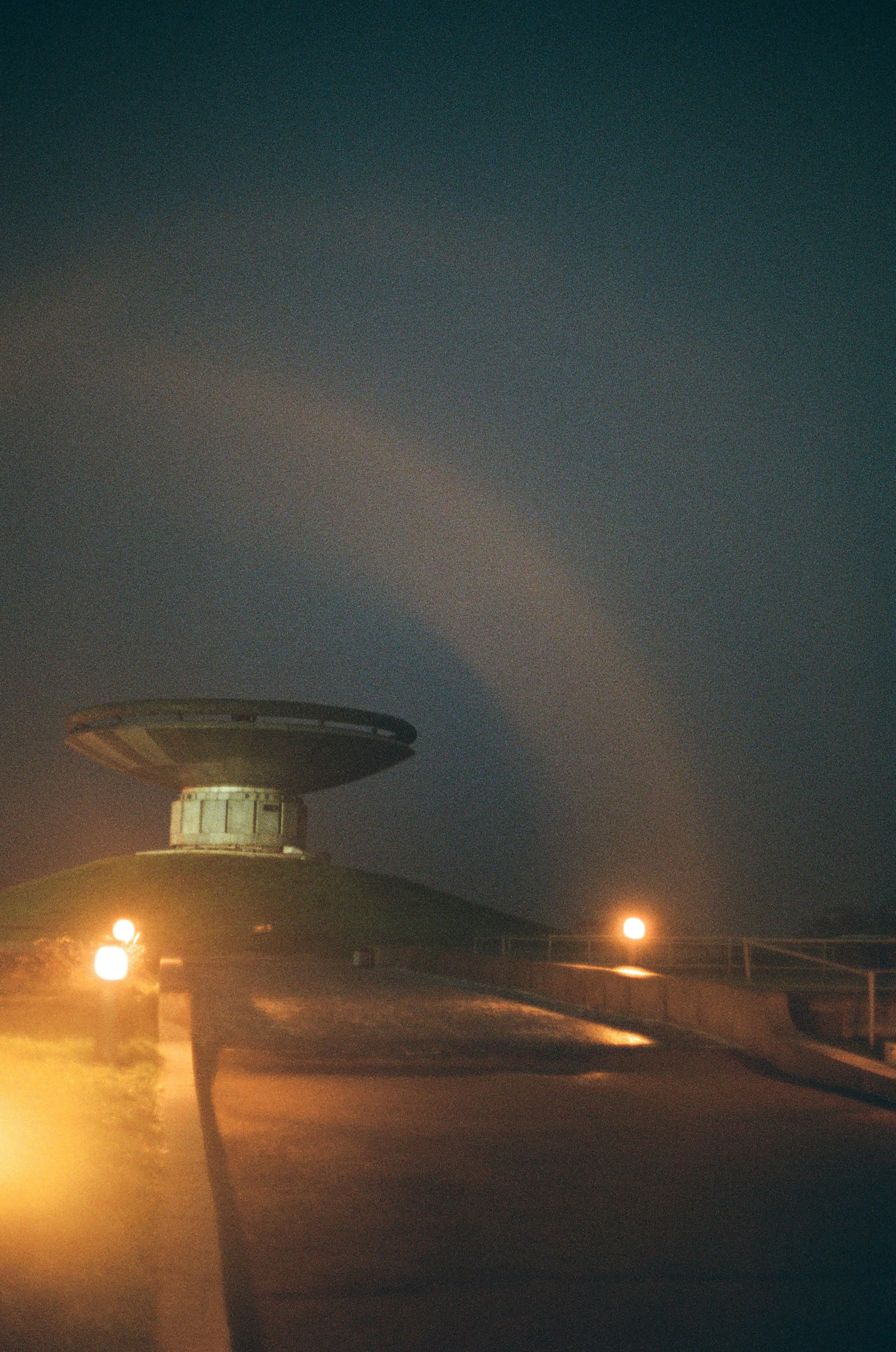 Futuristic structure illuminated by ambient lights on a foggy night, creating a mysterious atmosphere.
