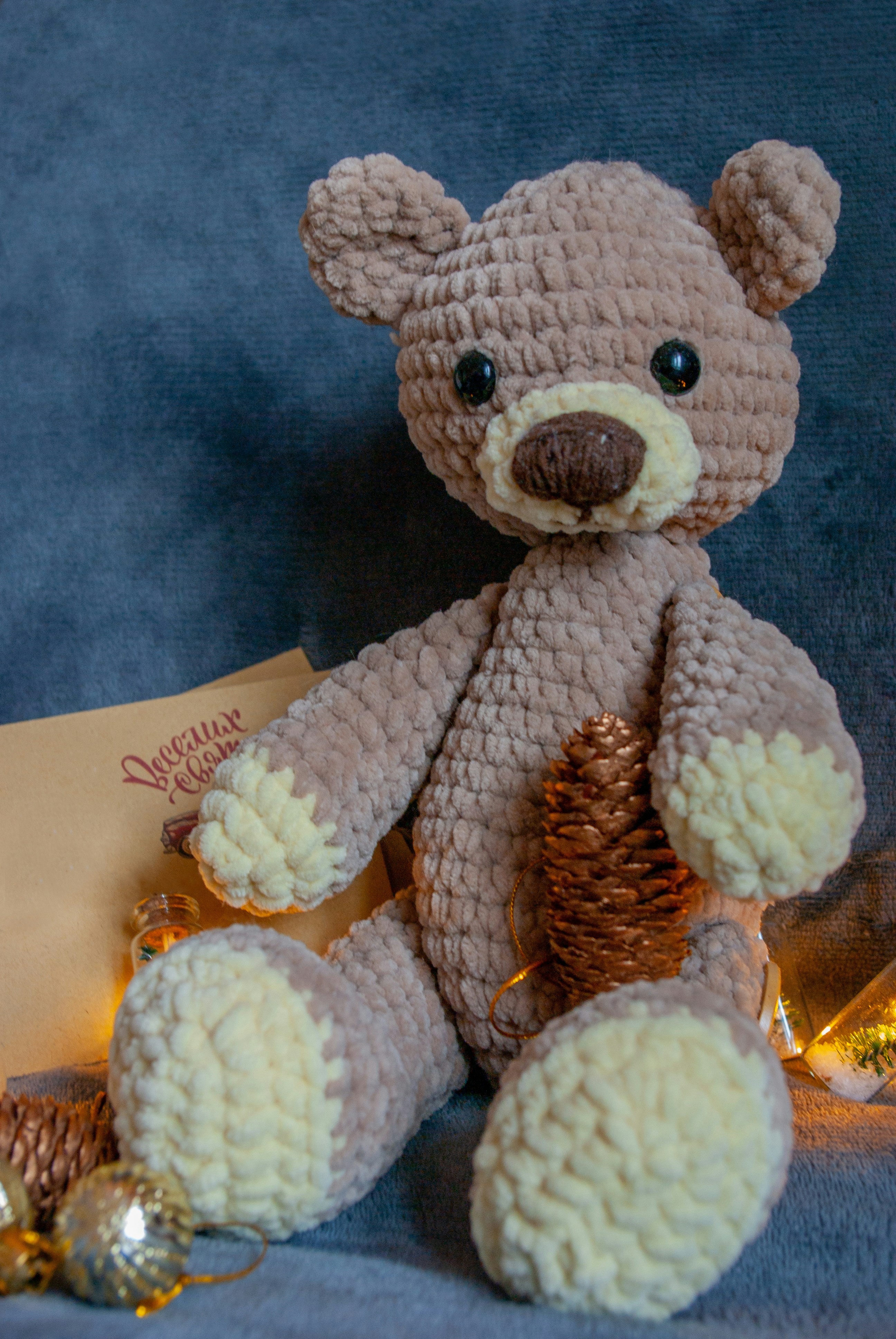 Soft, plush teddy bear seated among pinecones and festive decorations, exuding warmth and charm.