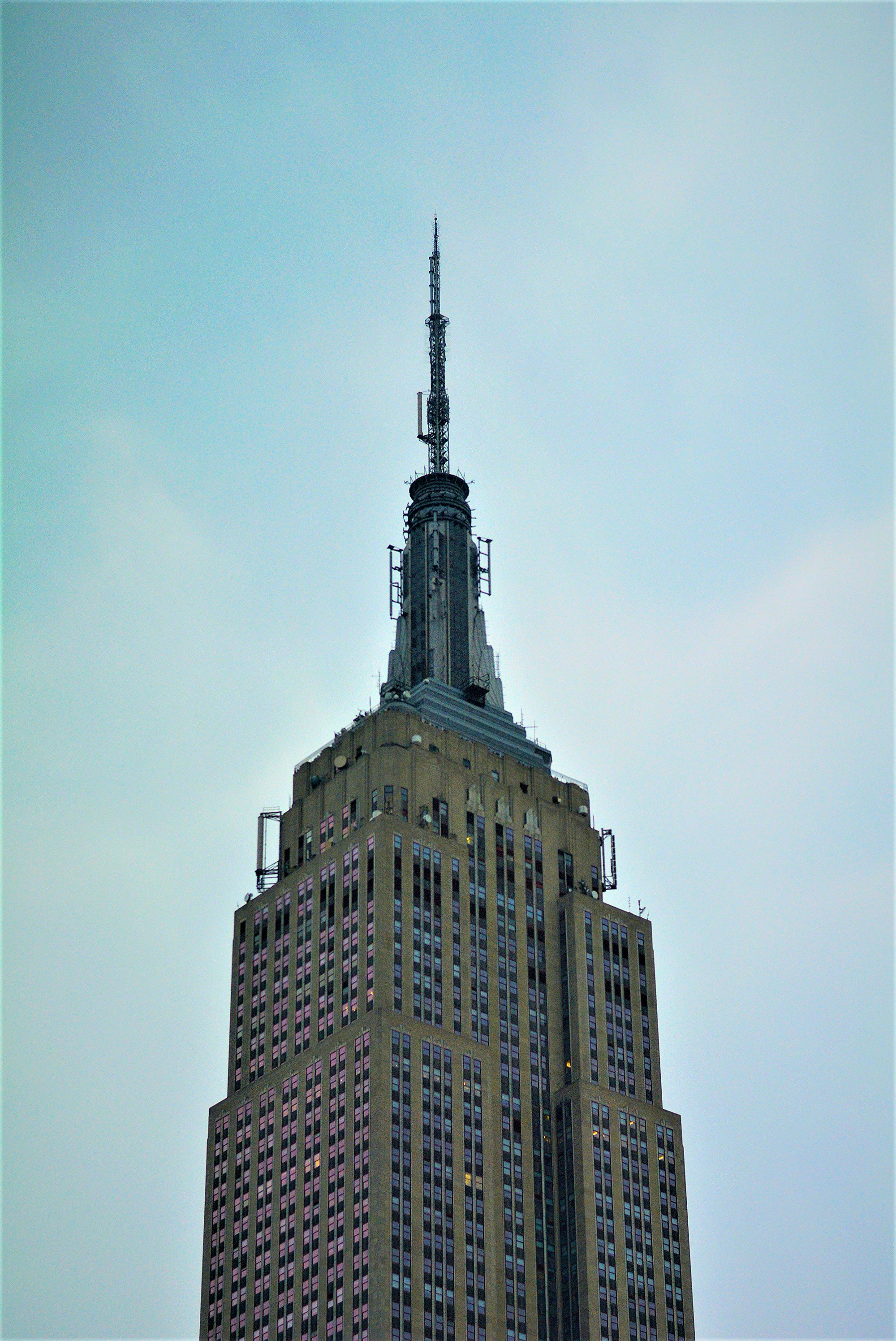 The Empire State Building's spire rises majestically against a soft, cloudy sky, showcasing its iconic Art Deco design.
