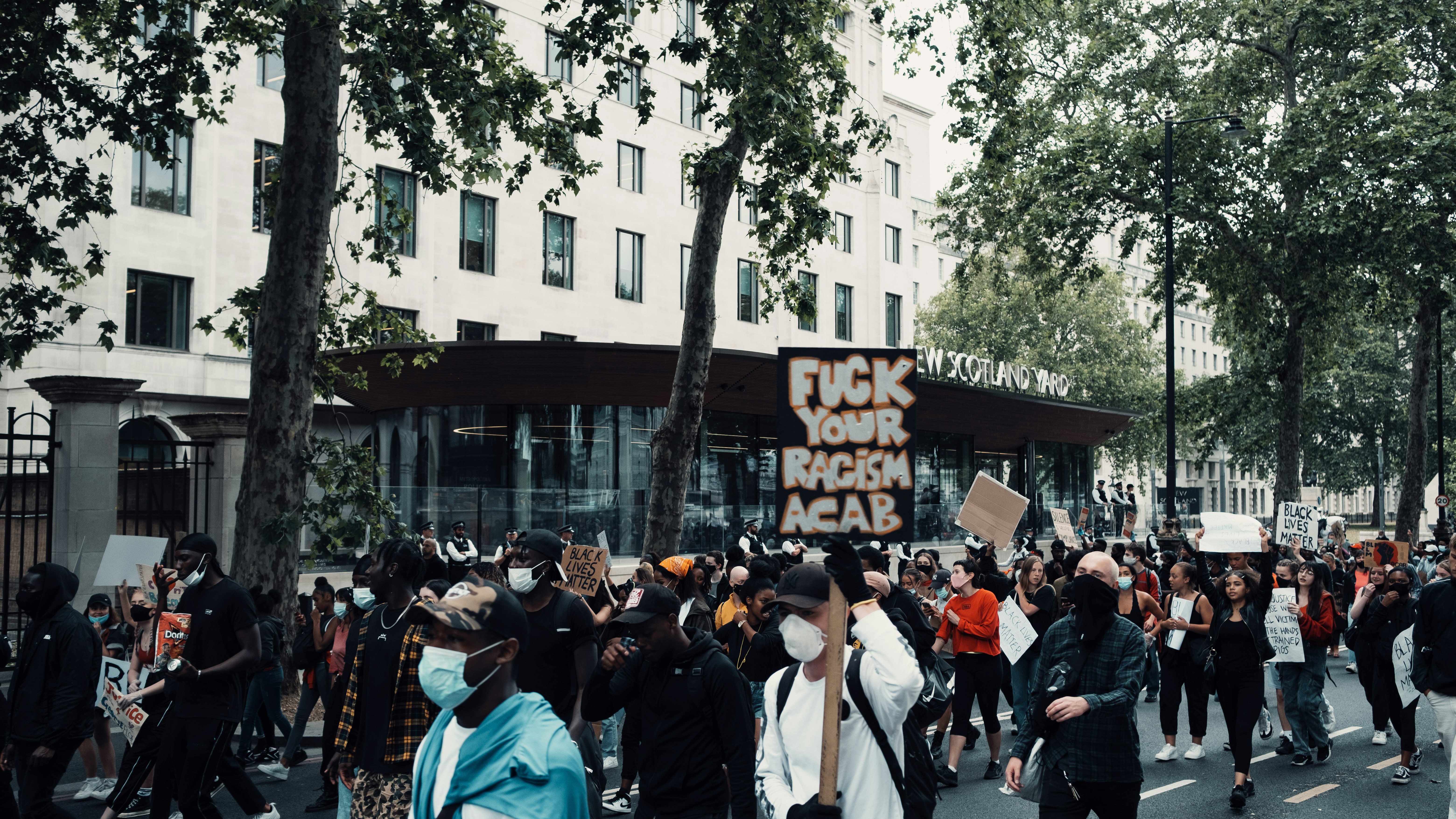 Crowd of protesters marching with signs advocating for racial equality and justice. The atmosphere is charged with determination.
