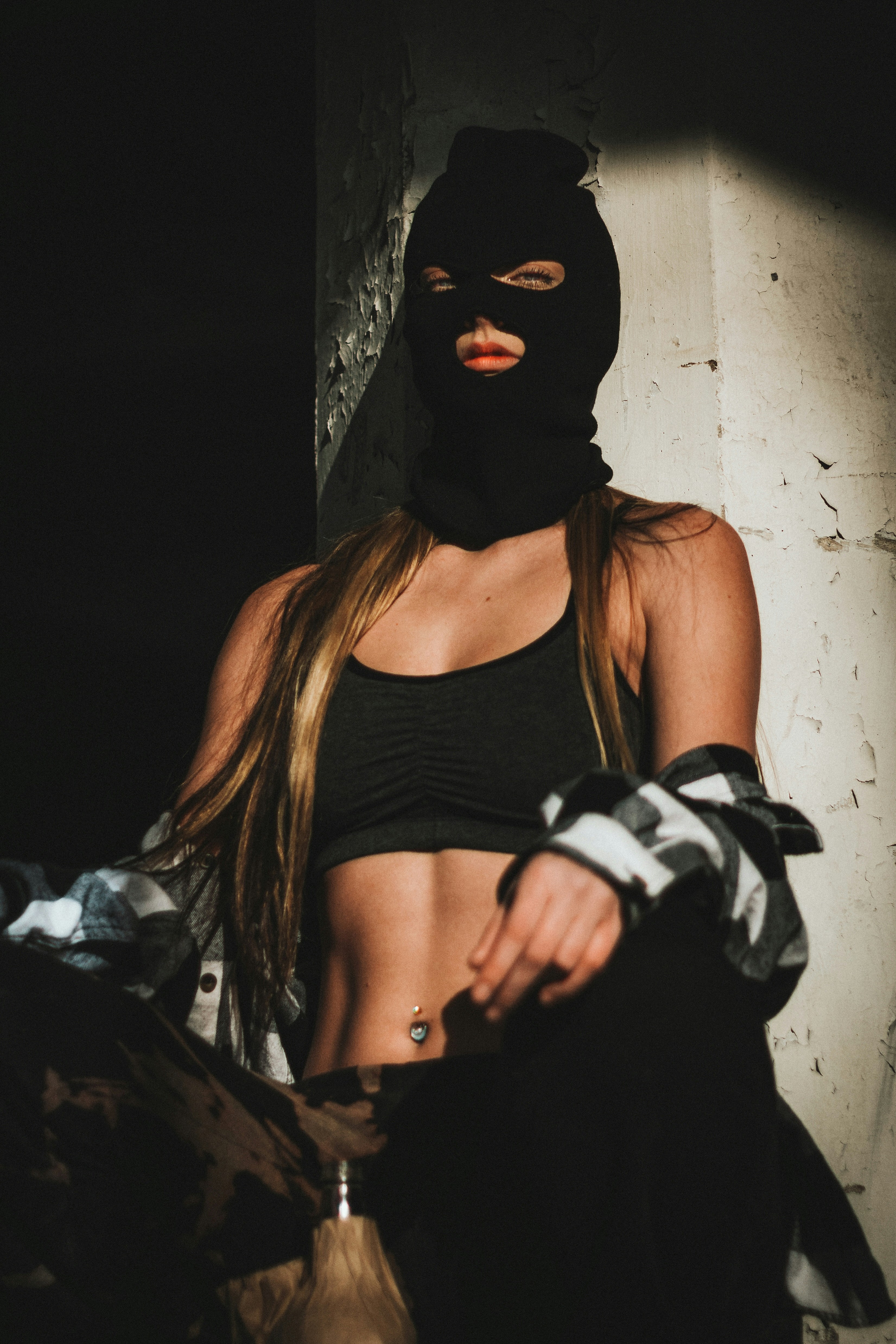 A figure in a black ski mask and athletic wear poses against a textured wall, embodying a blend of strength and enigma.