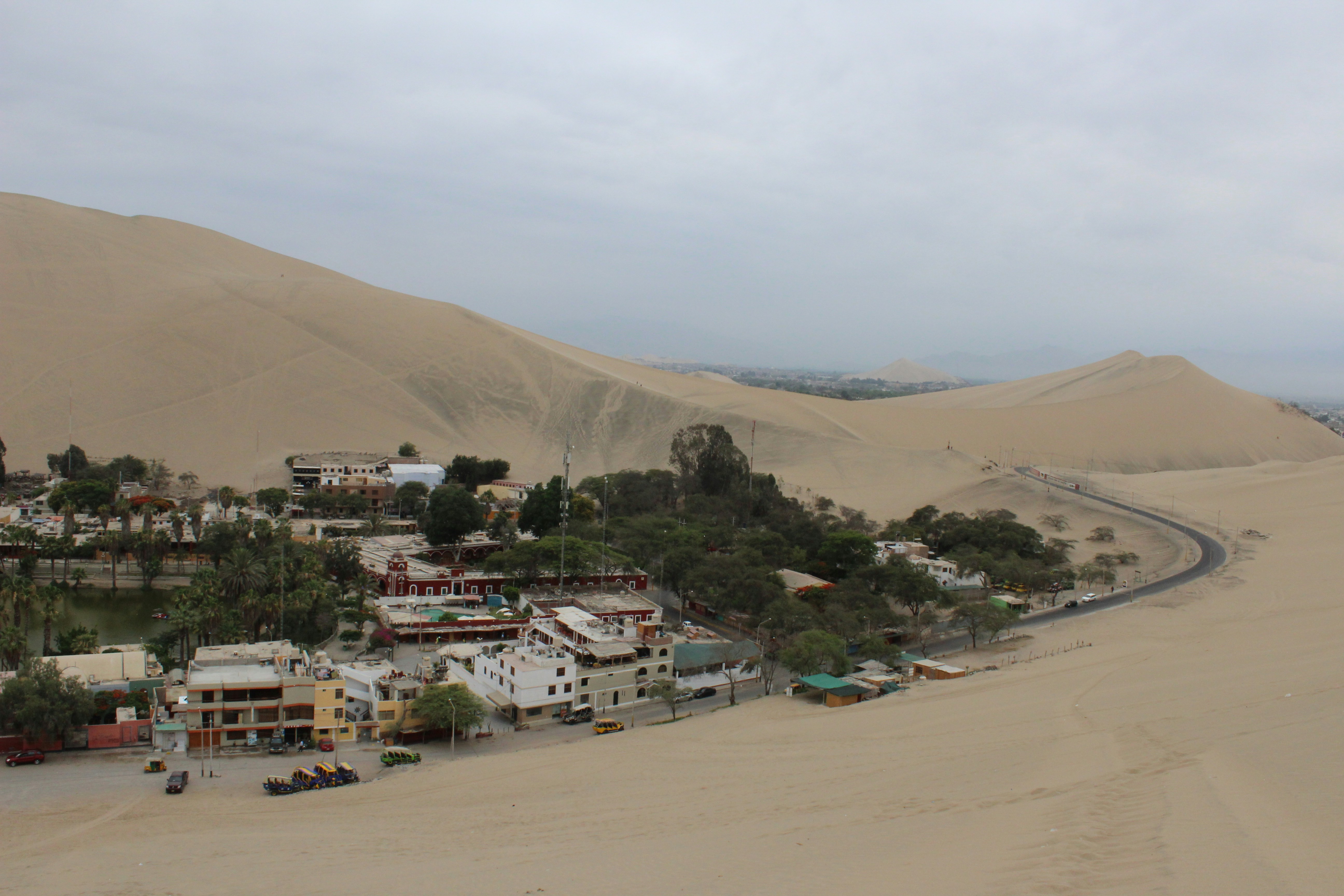 A small community nestled at the base of towering sand dunes, showcasing a blend of nature and human habitation.