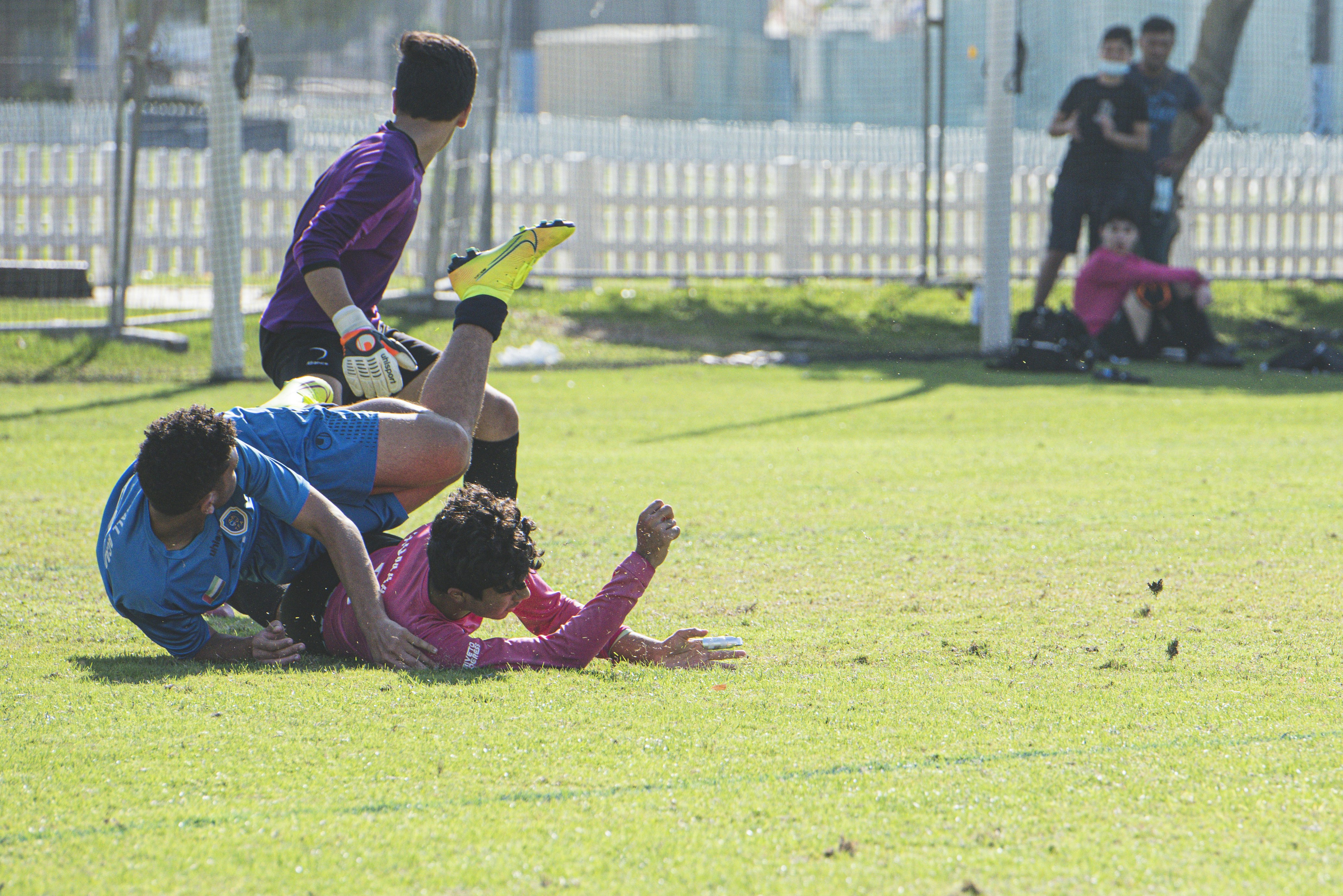 Two soccer players collide on the field while a goalkeeper observes the action. The intensity of the match is palpable.
