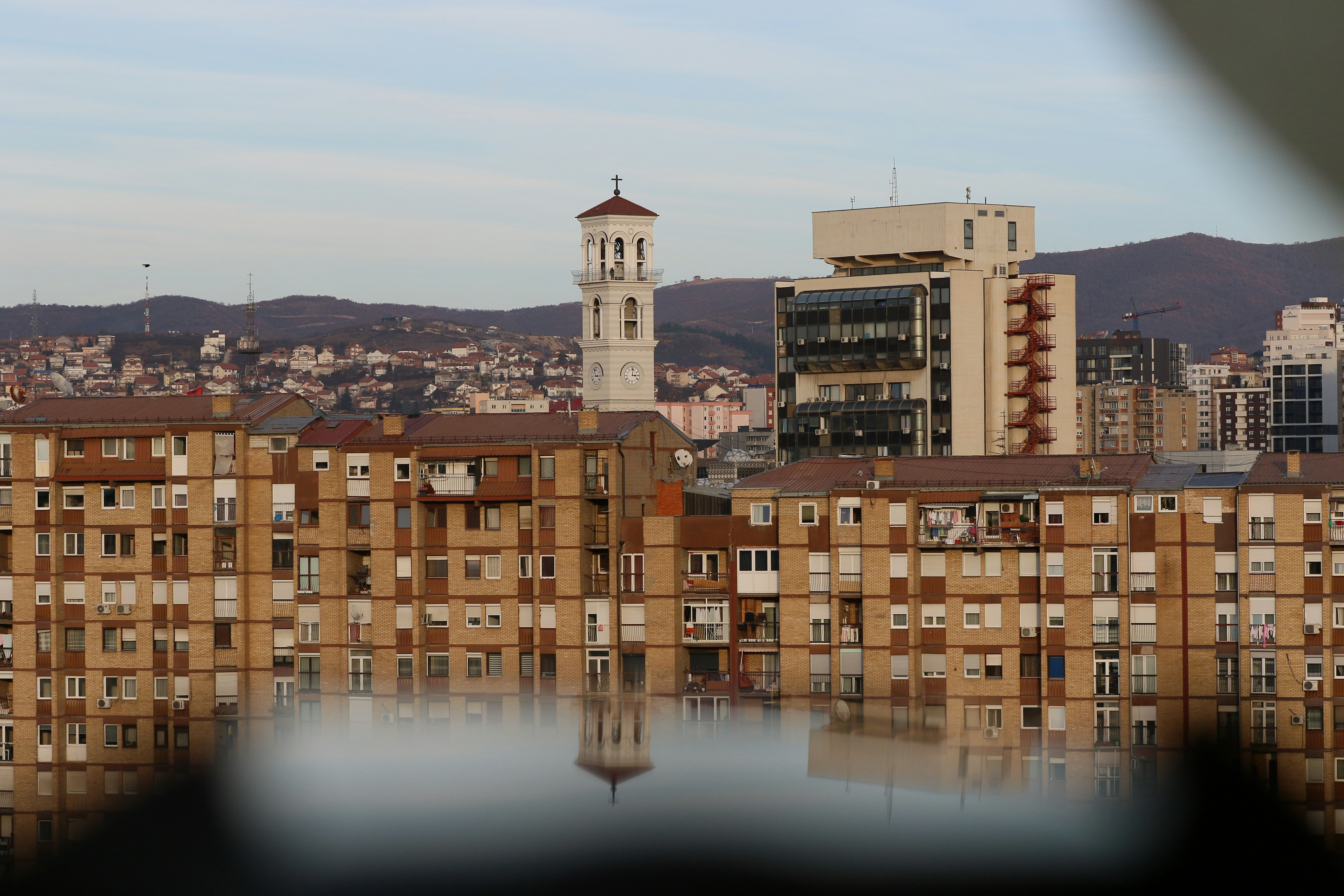 Mirrored Cityscape: Apartment Blocks and a Clock Tower Framed by a Blurred Foreground