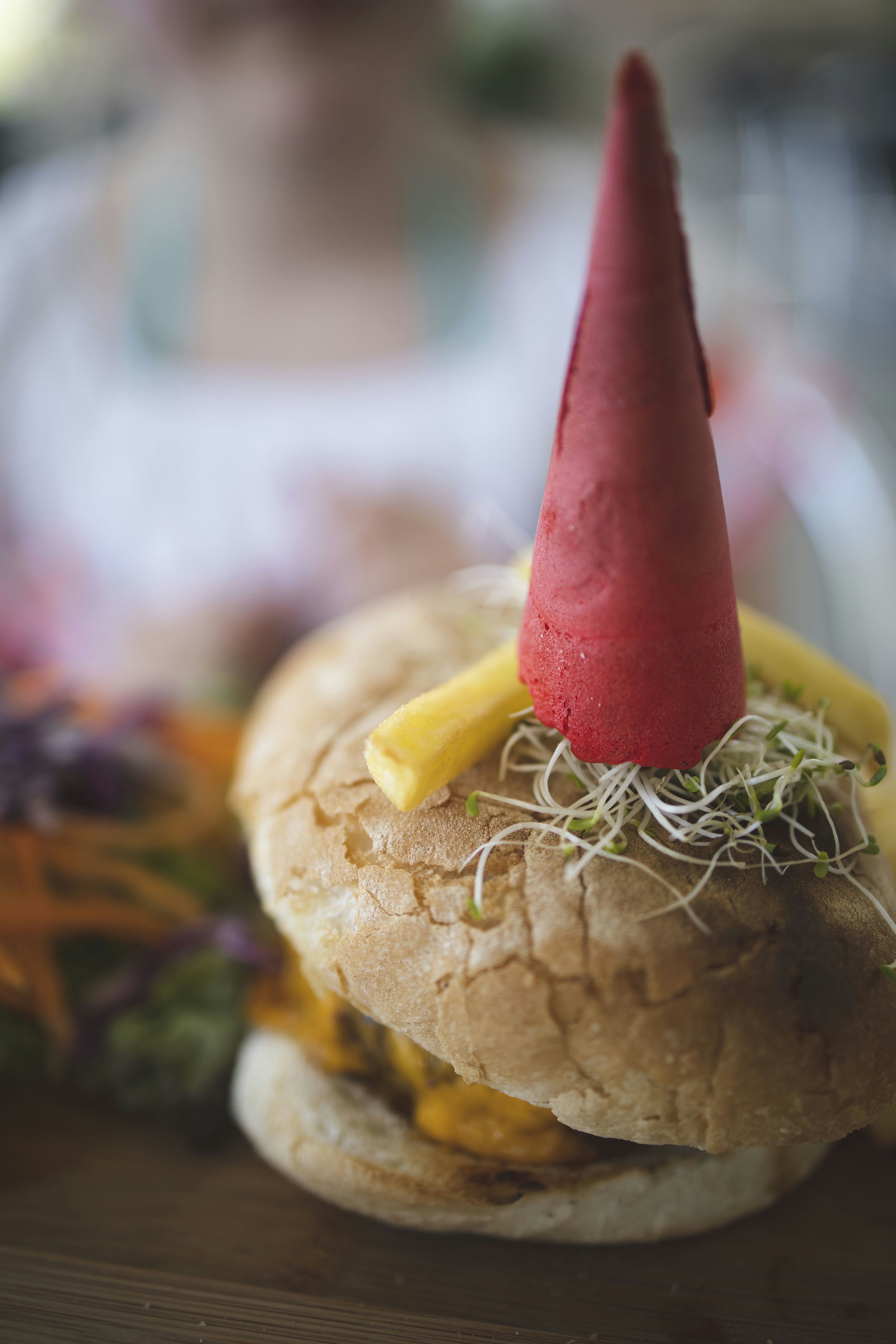 A creatively assembled burger topped with a vibrant red cone and yellow slice, accompanied by a colorful salad. Perfect for a playful dining experience.