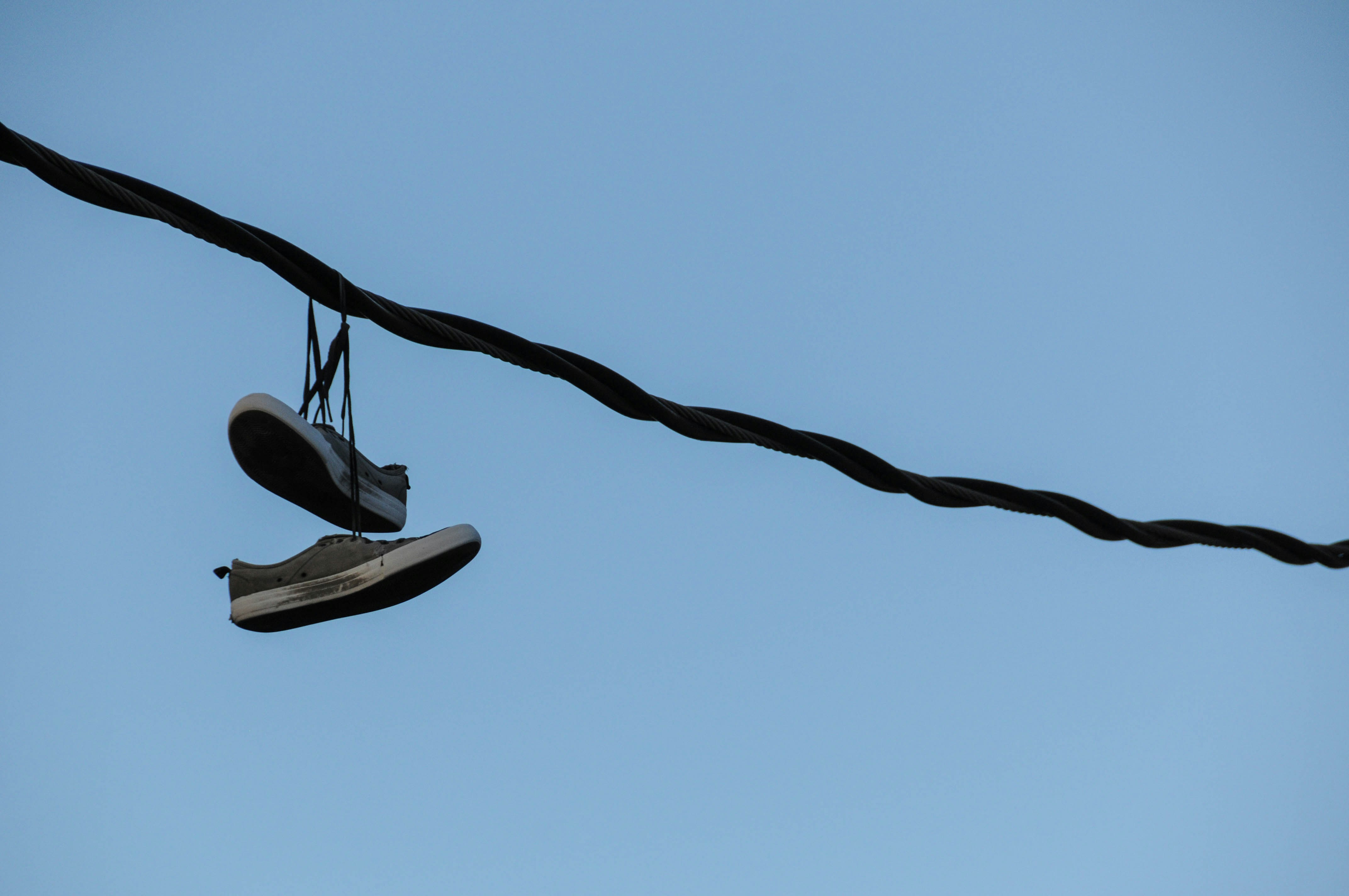 Old sneakers hanging from a power line against a clear blue sky.