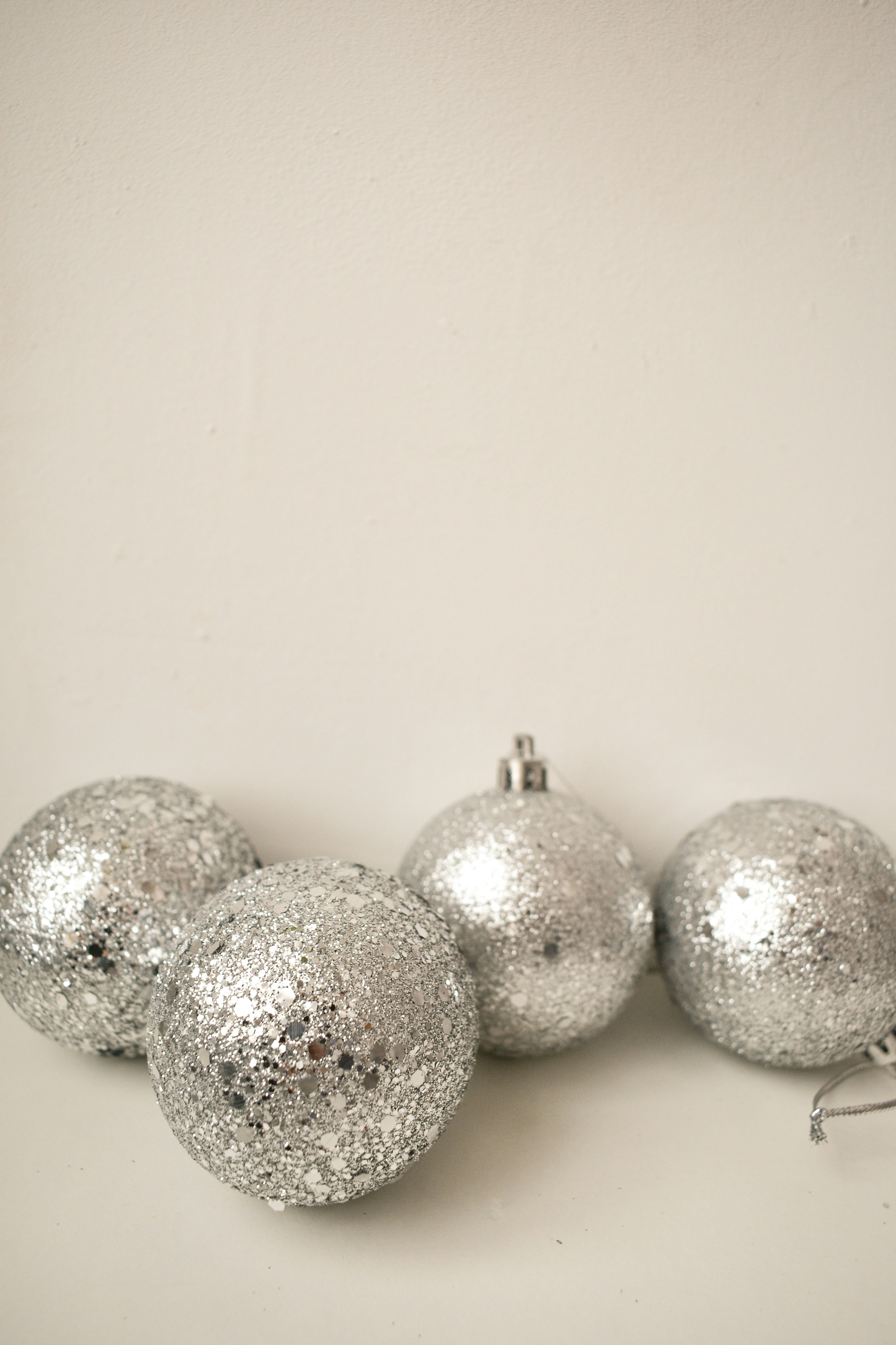Four sparkling silver ornaments resting on a neutral background, reflecting light with their textured surfaces.