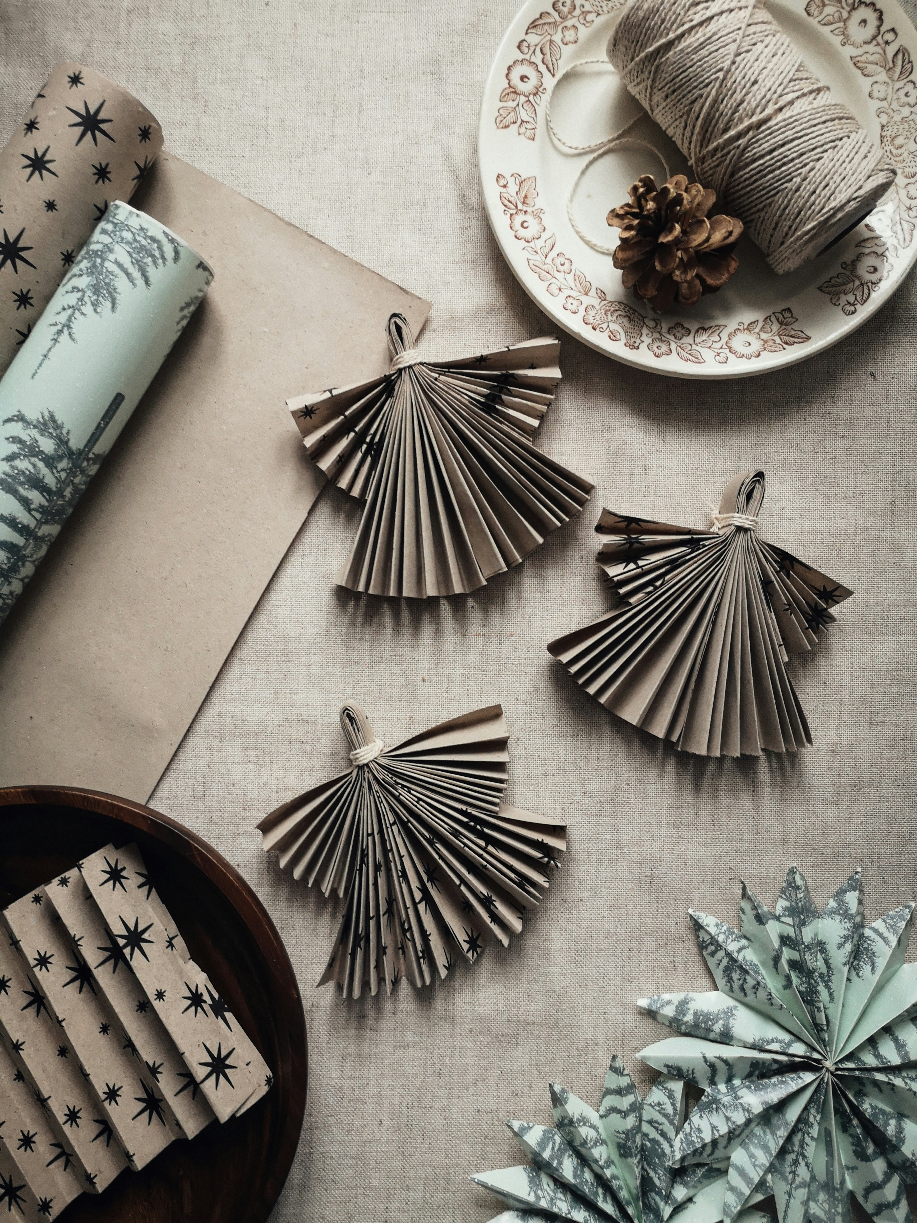 Handcrafted paper ornaments arranged on a textured surface, showcasing intricate folding techniques. A spool of twine and natural elements add to the crafting ambiance.