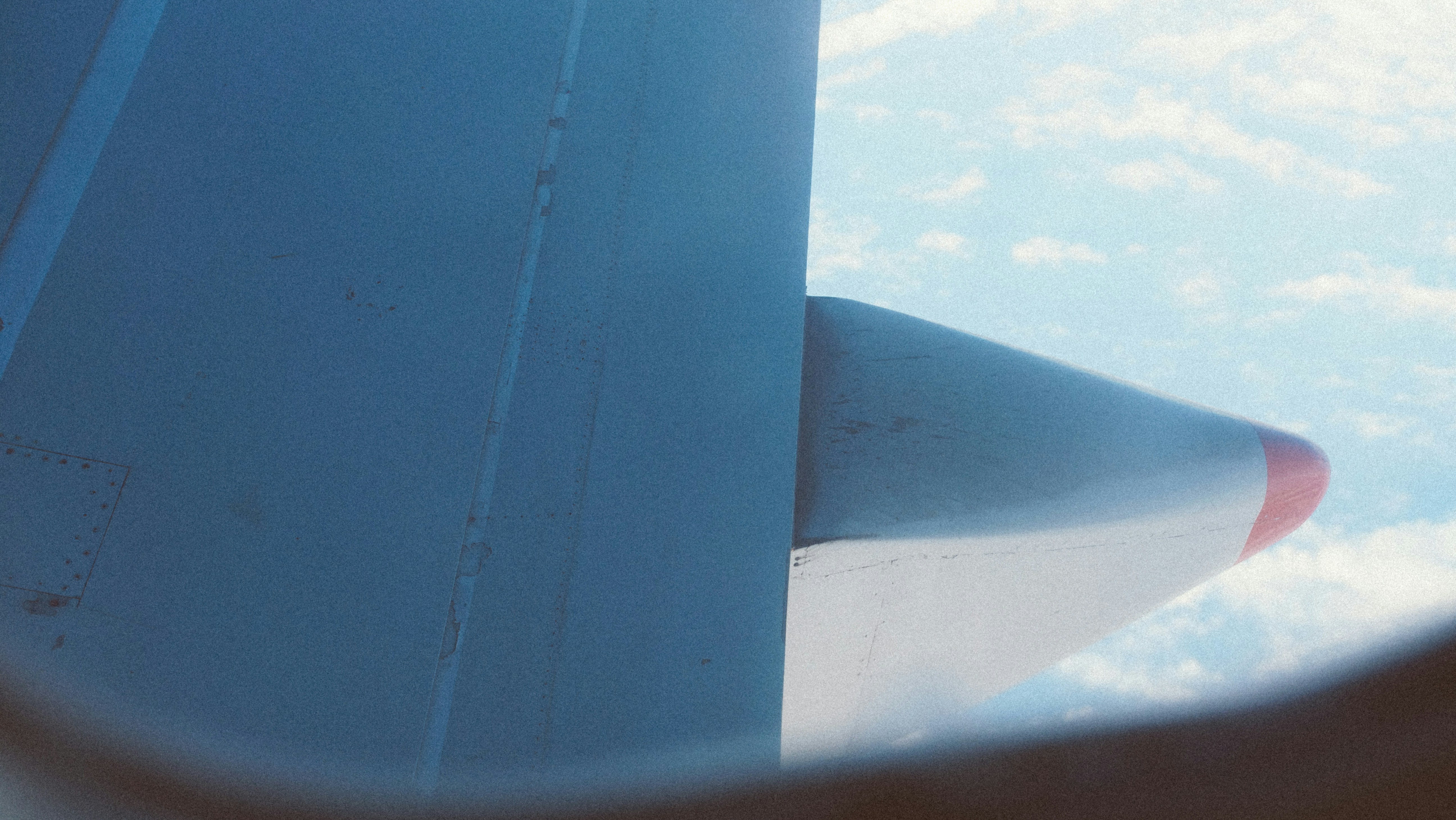 Aircraft wing with a red-tipped engine against a backdrop of soft clouds and blue sky.