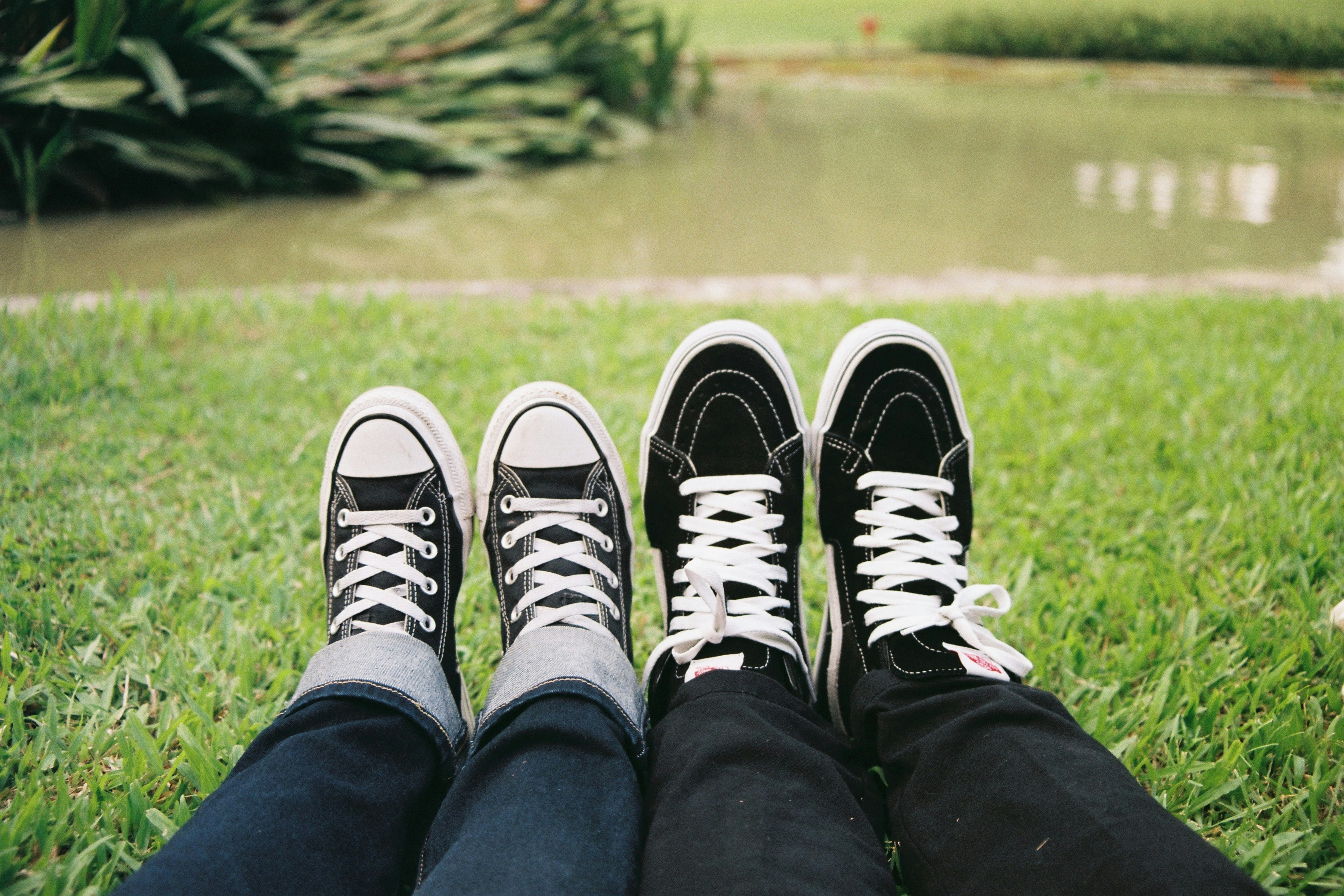 Two pairs of sneakers resting on lush green grass by a tranquil pond, symbolizing connection and leisure.